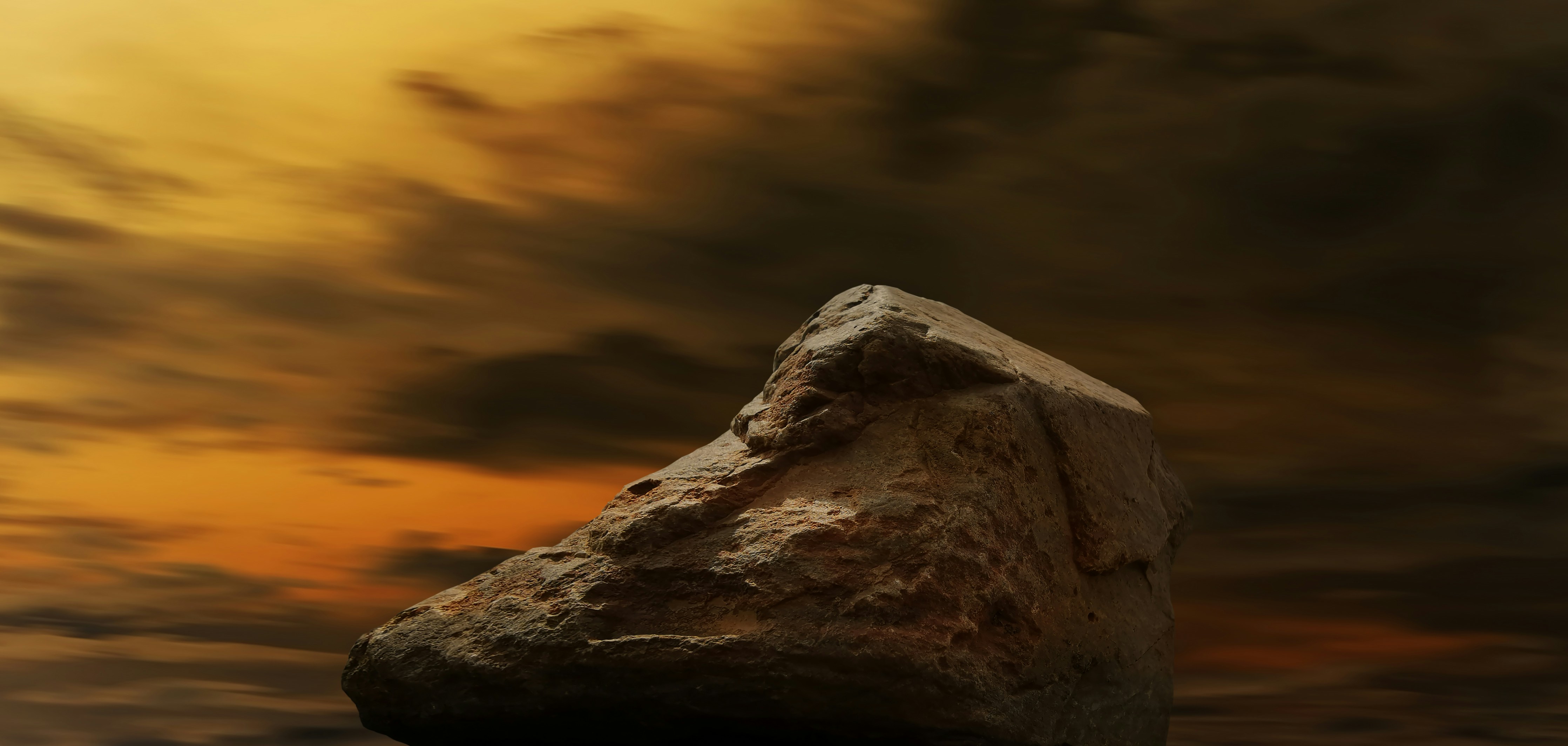 A solitary rock formation stands against a dramatic sky painted in hues of orange and yellow, evoking a sense of tranquility and solitude.