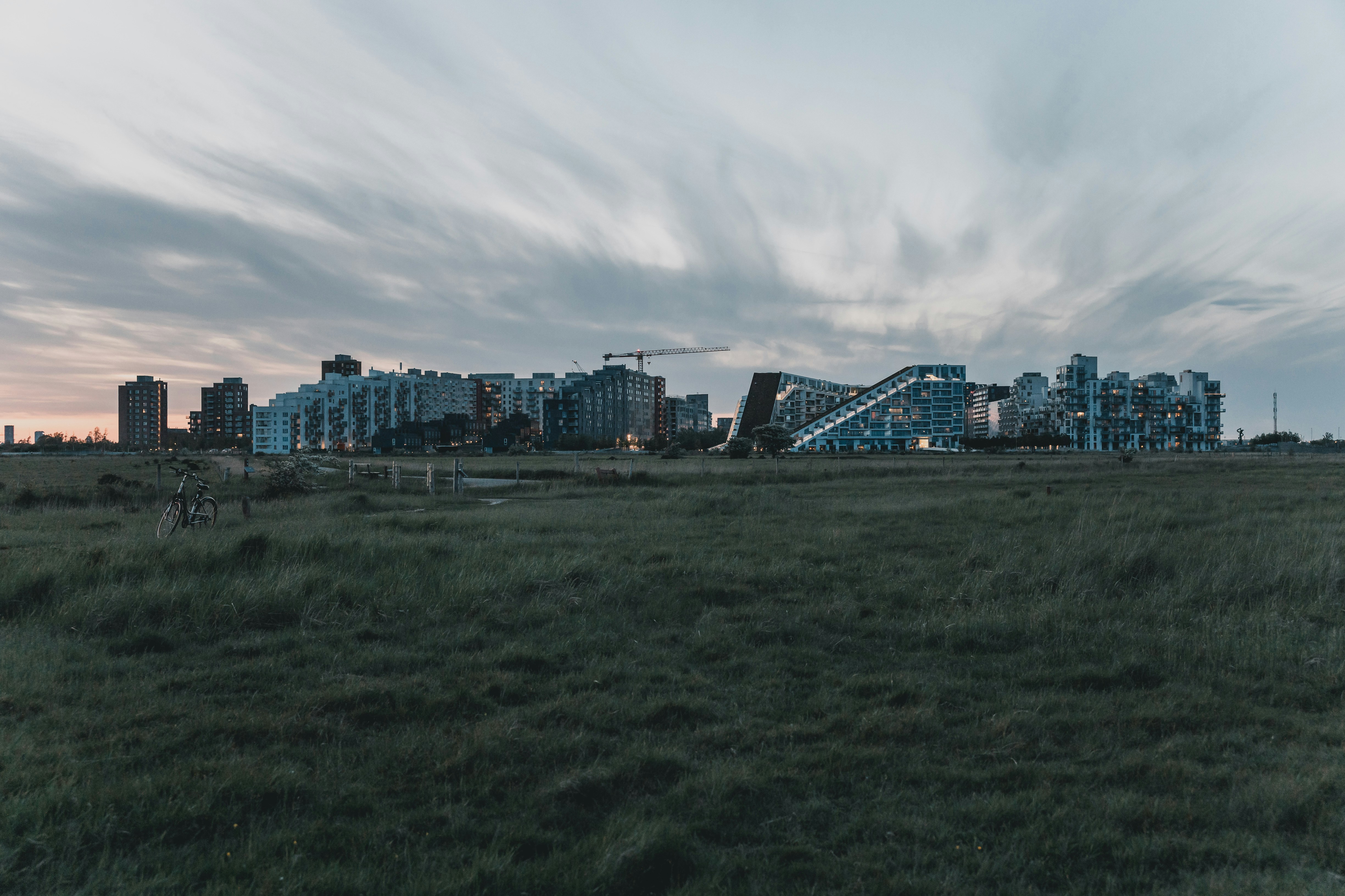 Modern architecture silhouetted against a twilight sky, with a grassy foreground and a hint of a bicycle on the left.