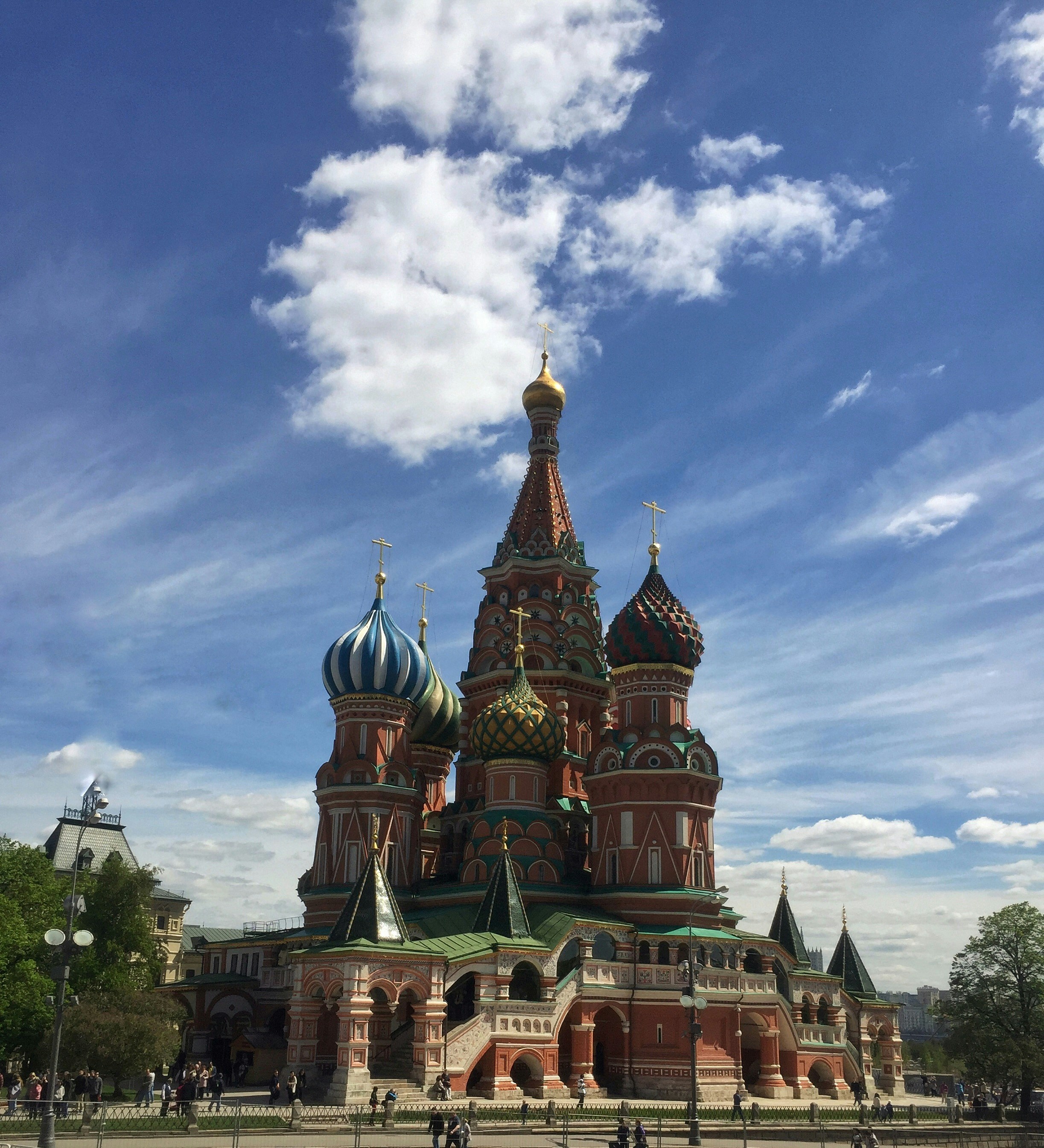 St. Basil's Cathedral showcases its iconic onion domes under a bright blue sky, surrounded by lush greenery and a bustling square. The architectural details reflect a rich history.