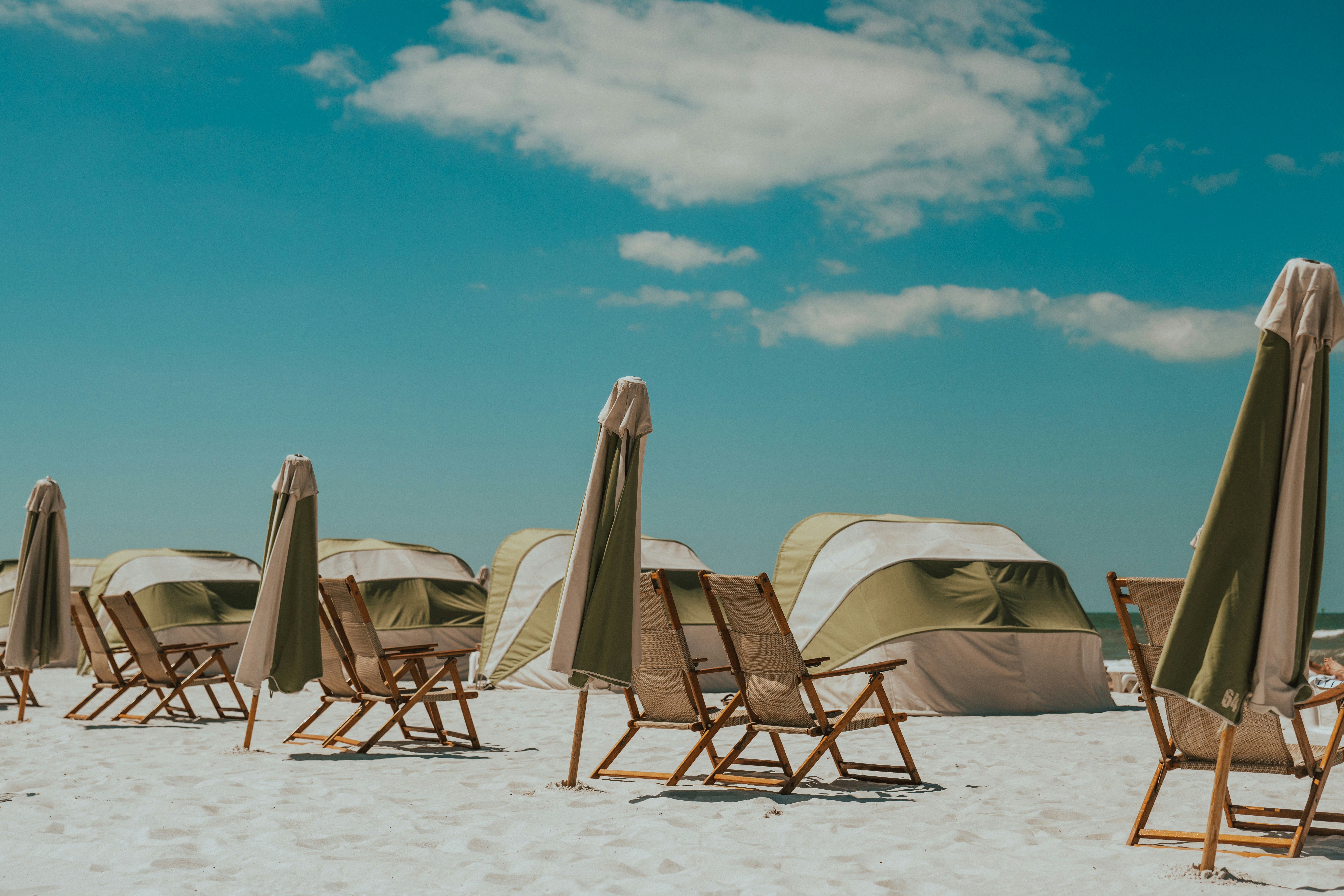 Wooden chairs and green umbrellas line a pristine sandy beach with a bright blue sky overhead.