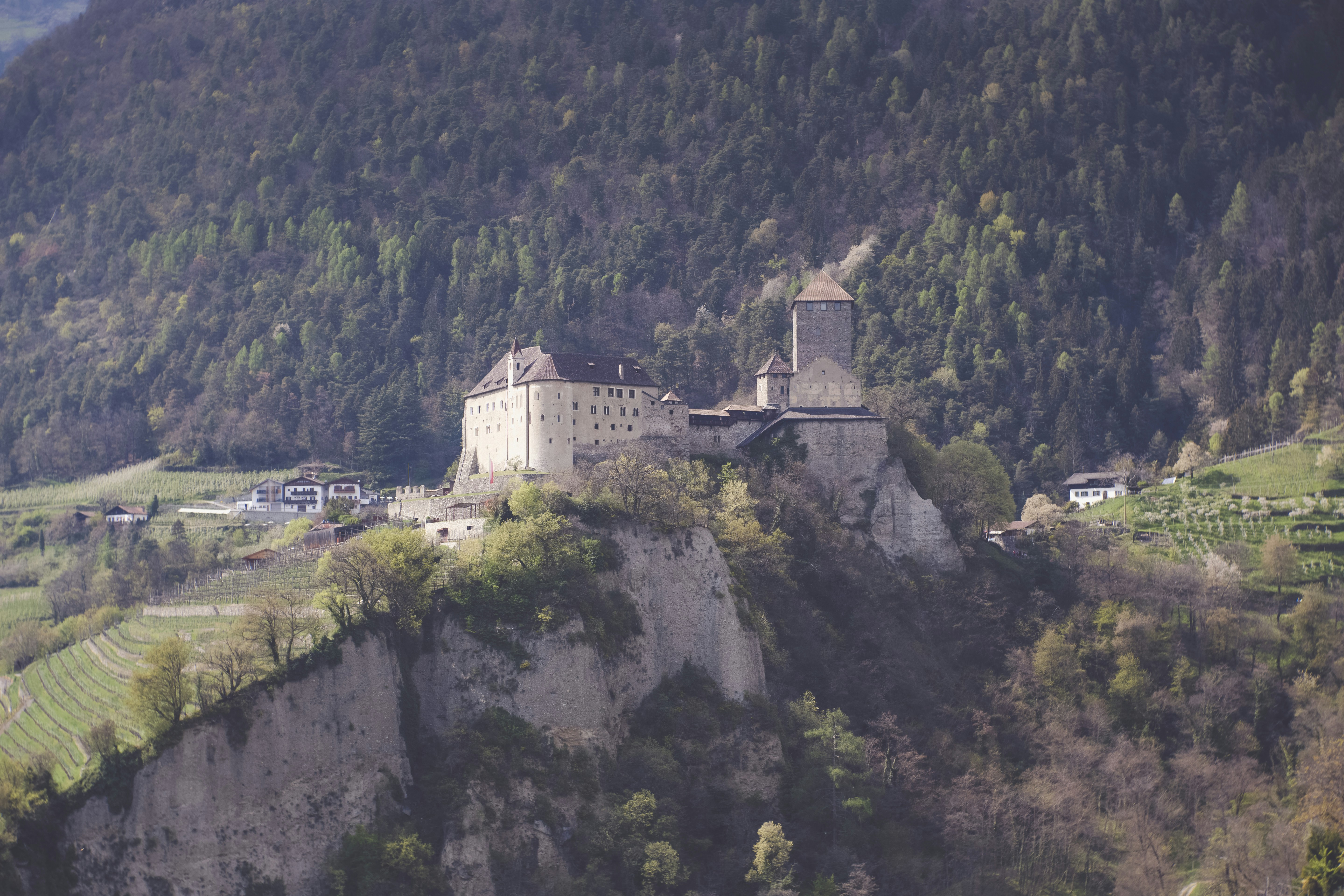 Historic stone fortress perched on a rugged cliff surrounded by lush greenery under clear skies.