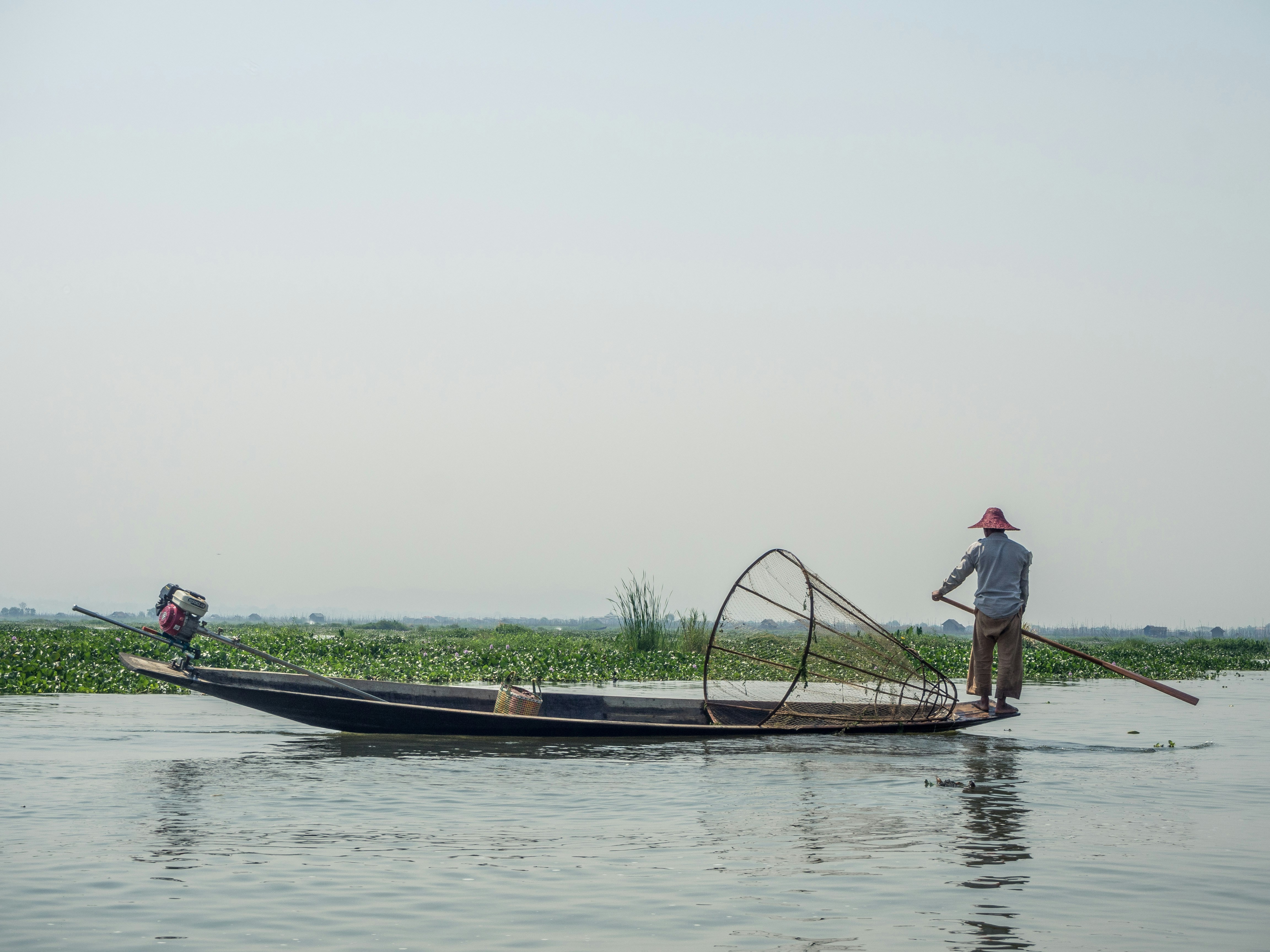 Fisherman skillfully maneuvering a traditional boat through a tranquil waterway, surrounded by lush vegetation.