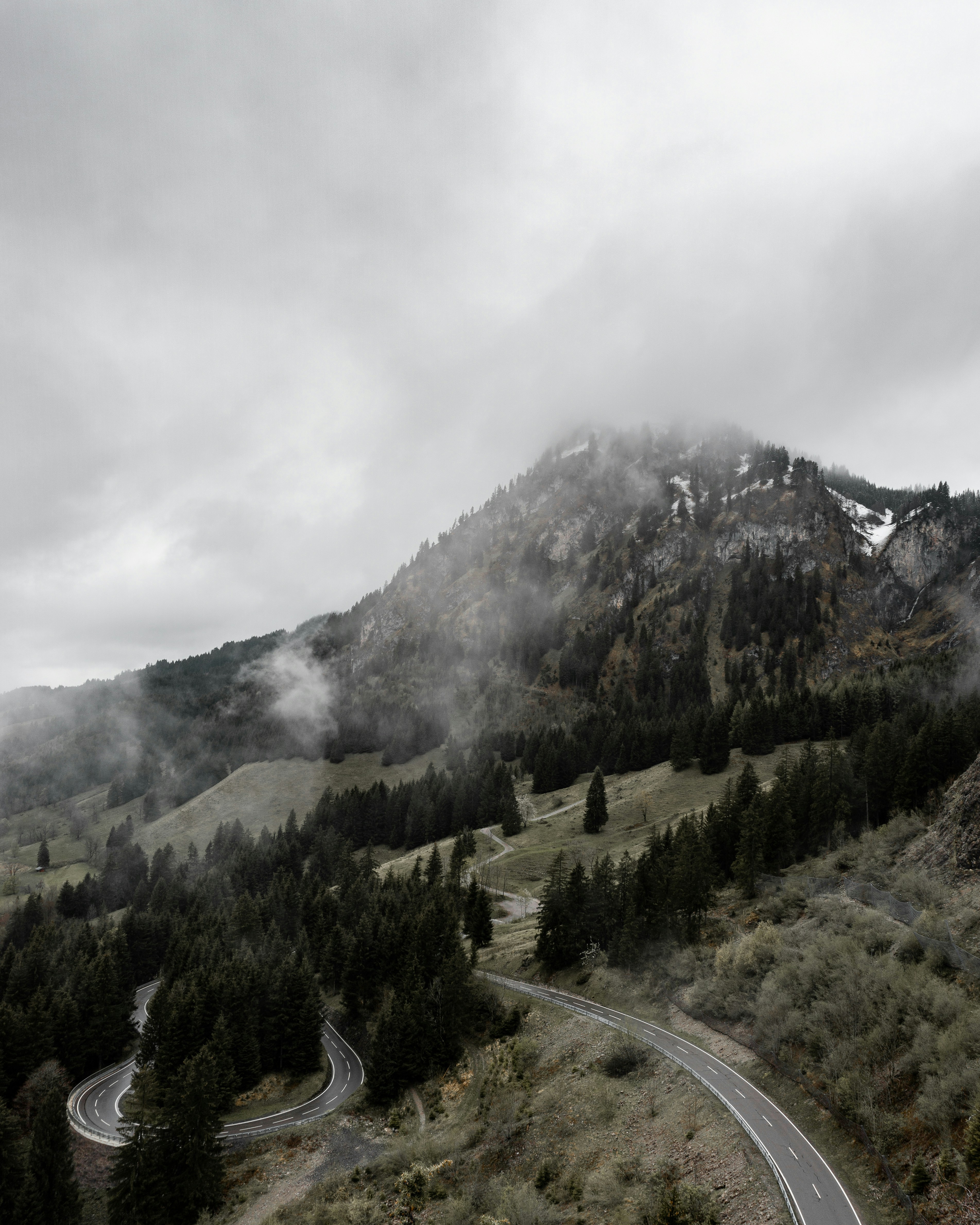 Curved road meandering through dense forests and fog-covered mountains, showcasing the beauty of nature's contours.
