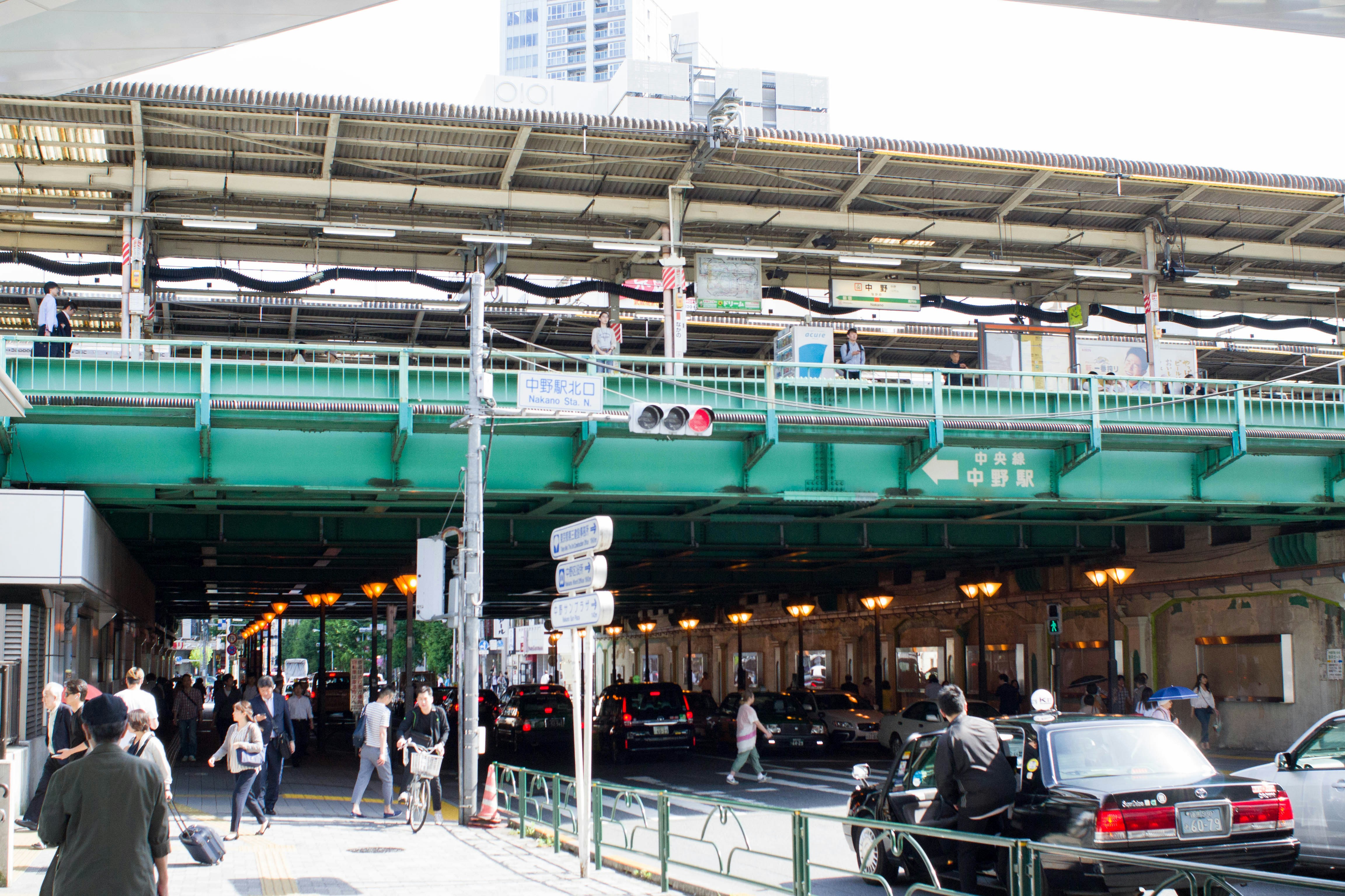 Busy urban scene featuring an elevated train station above a bustling street filled with pedestrians and cars.