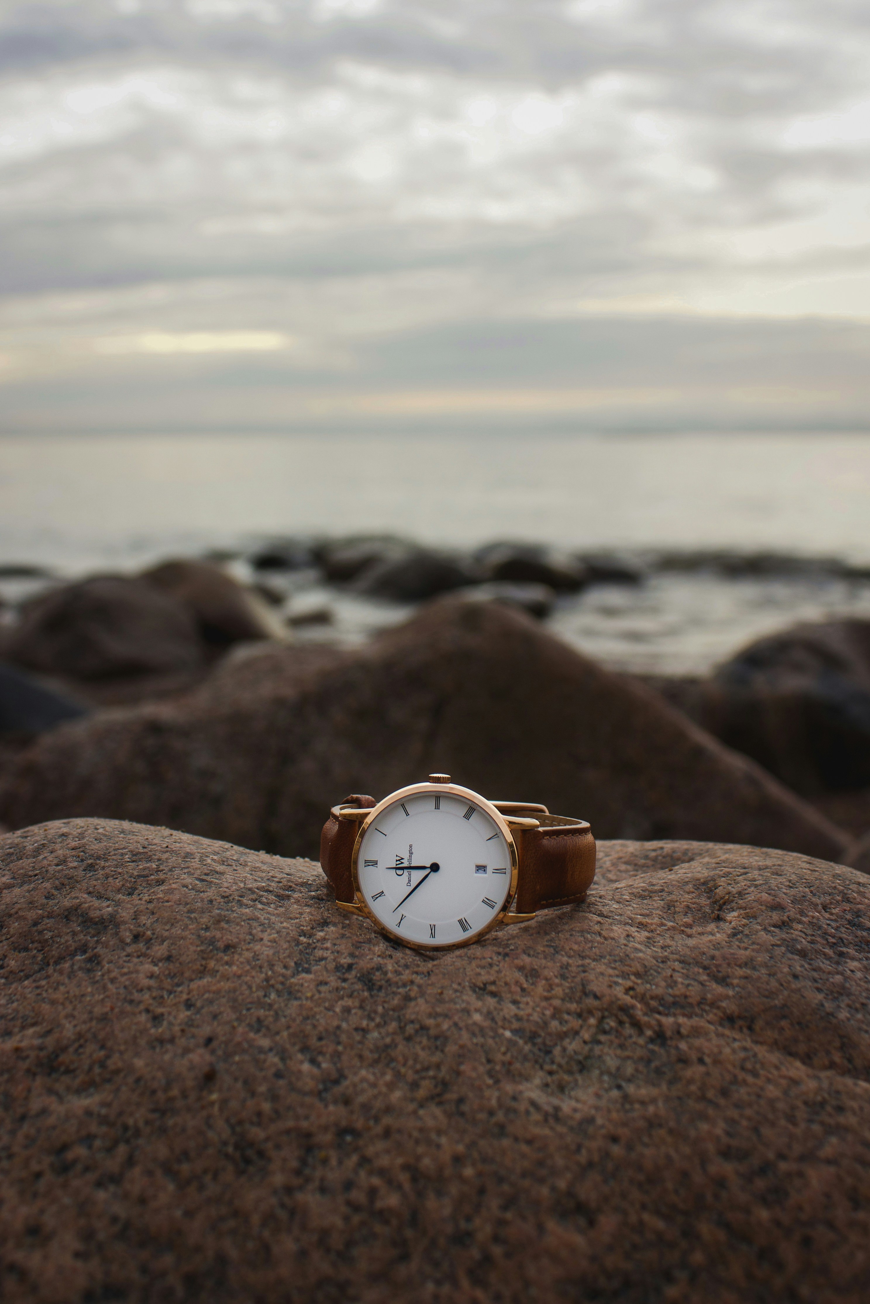 round gold-colored analog watch on rock near shore