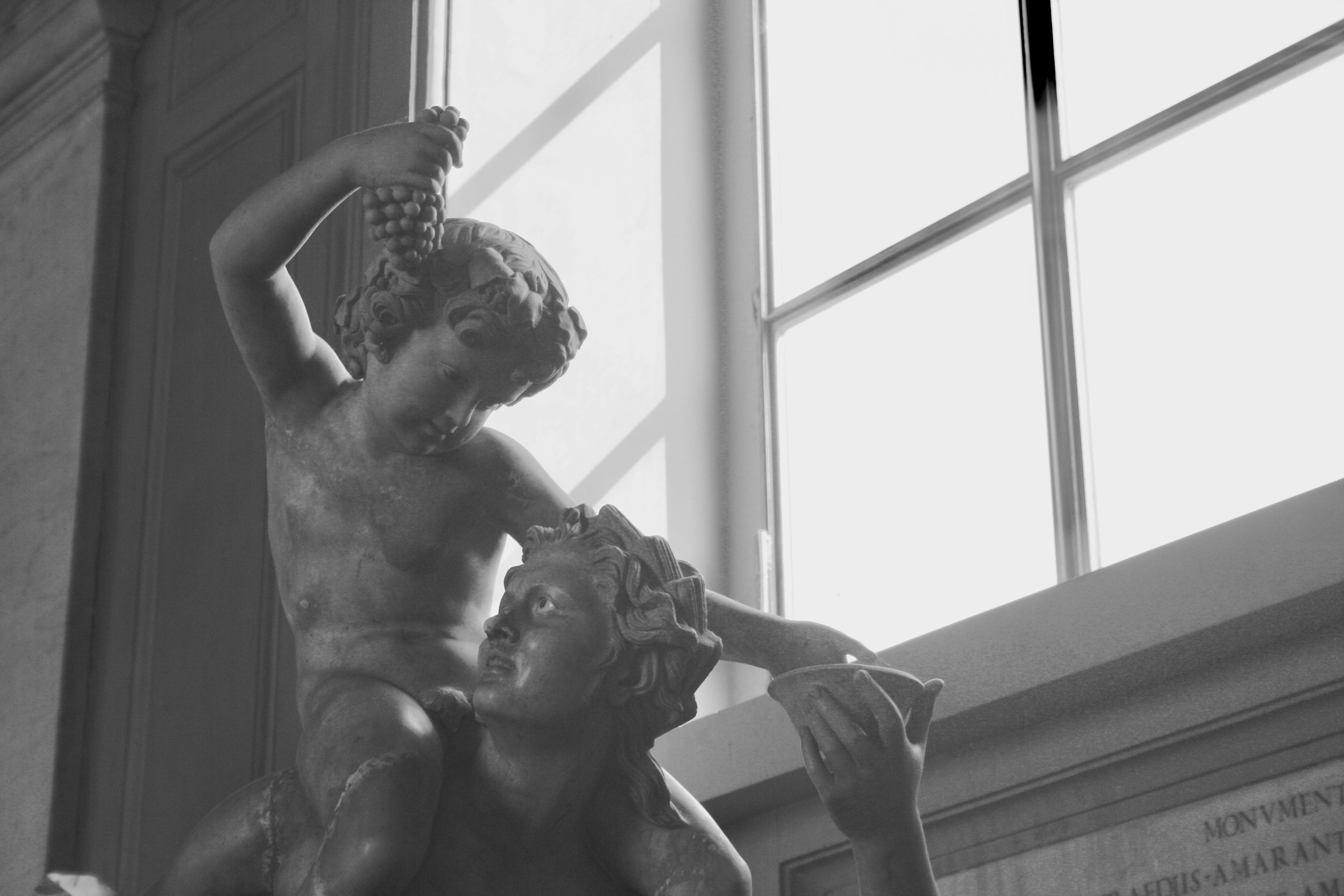 Sculpture of a cherub offering grapes, set against a large window.
