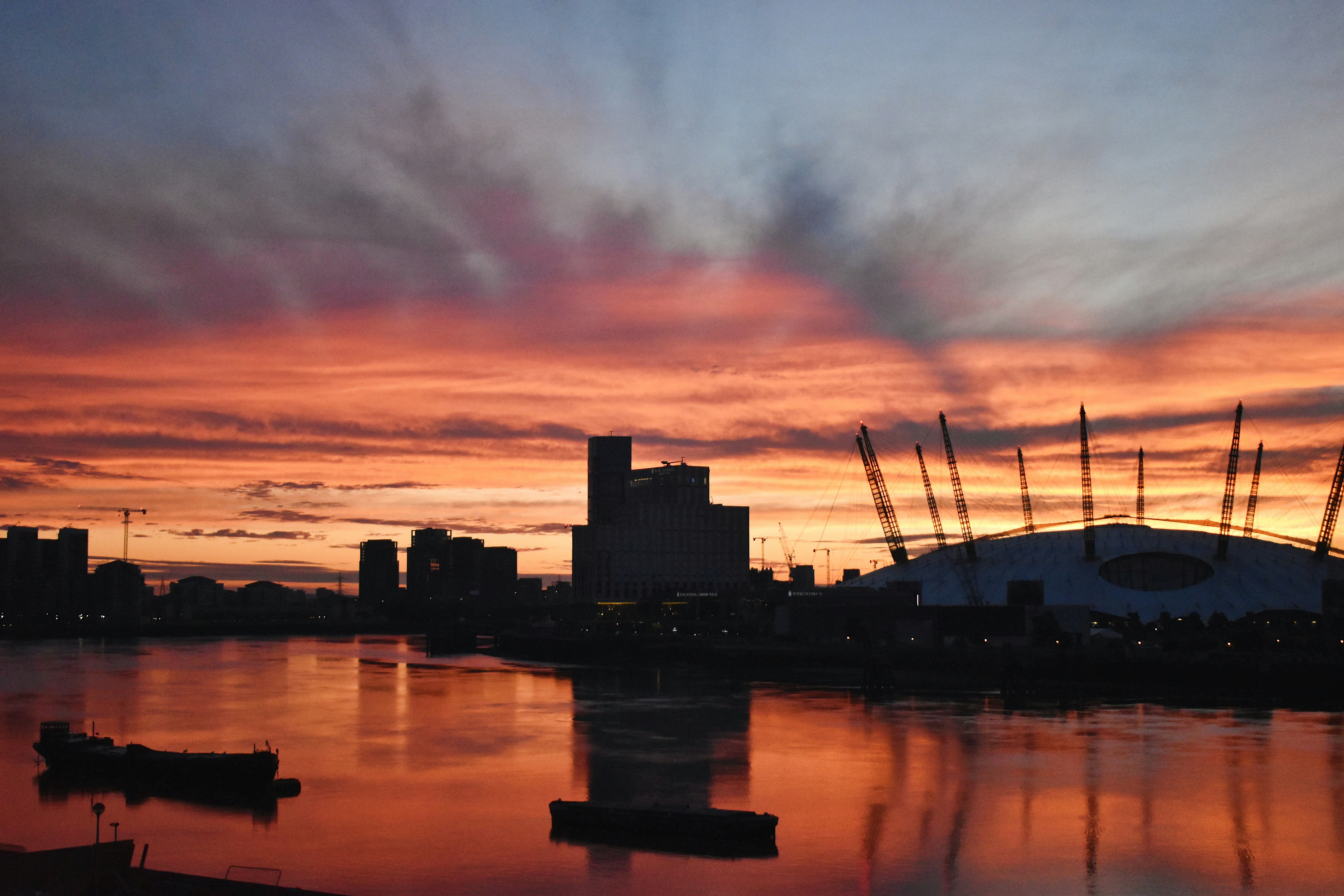 Vibrant sunset casting colorful reflections on the water, with silhouetted buildings and a distinctive architectural structure in the foreground.