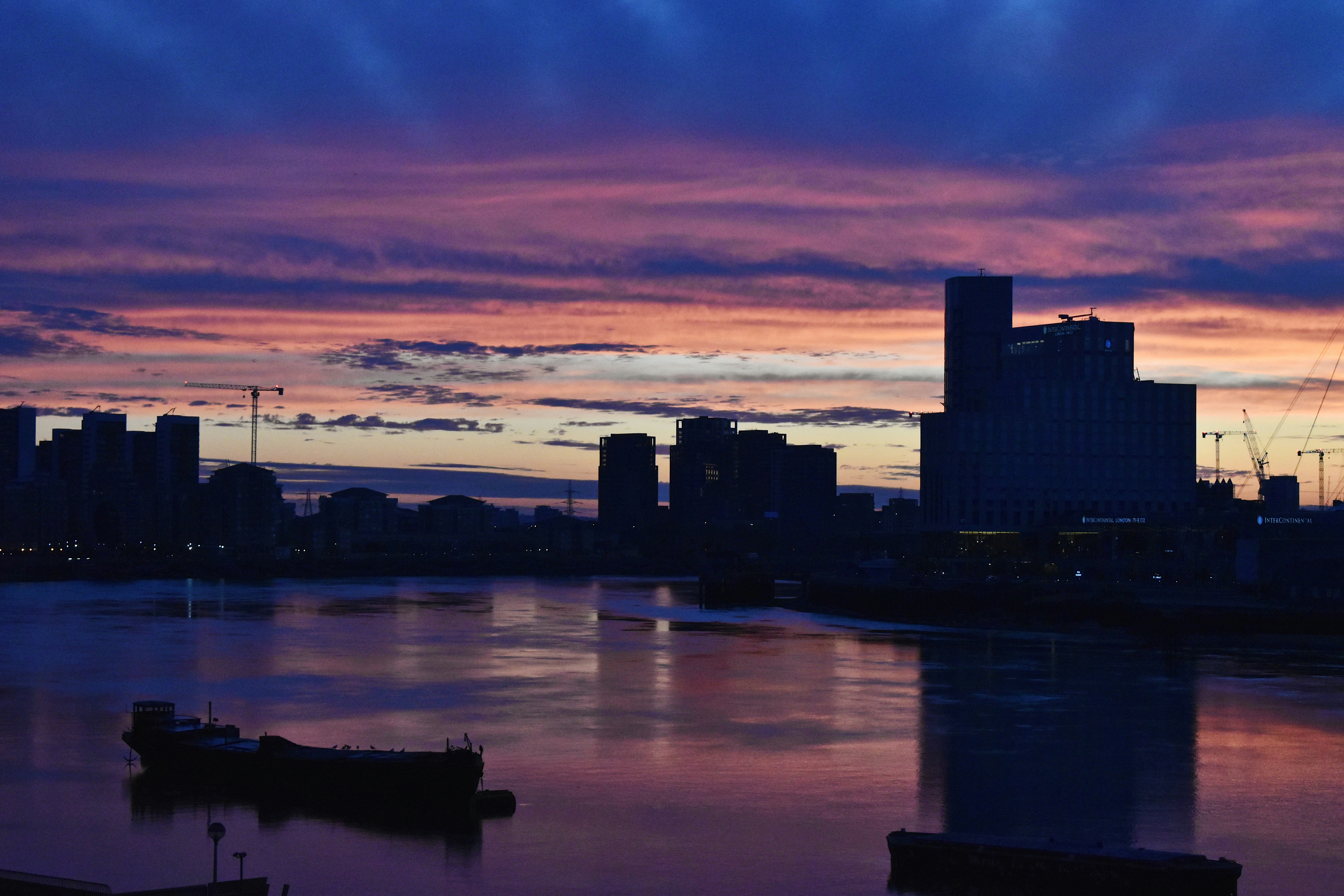 Silhouetted skyline against a vibrant twilight sky, with reflections shimmering on the water's surface.