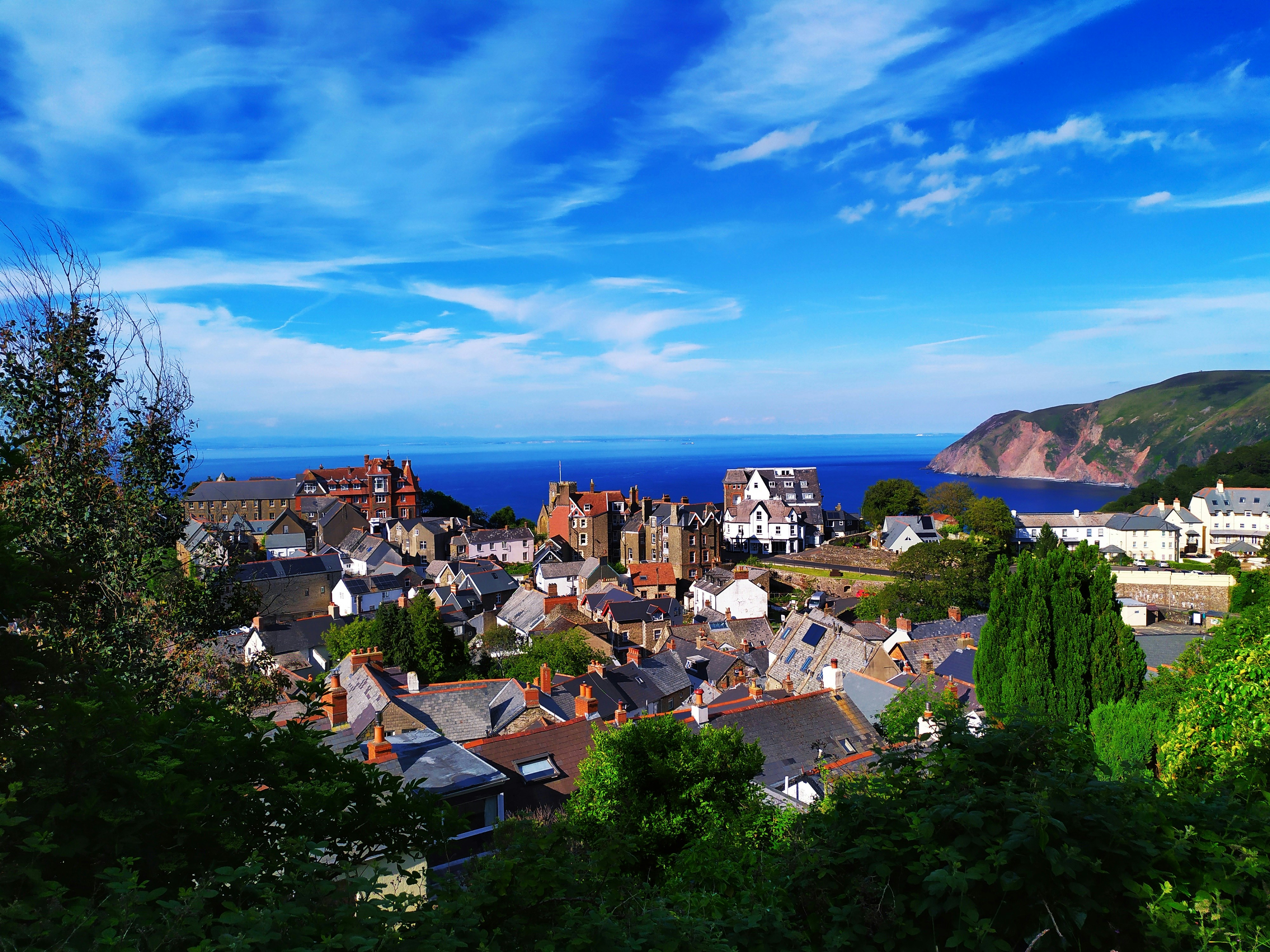 A panoramic view of a coastal village with charming rooftops nestled against a backdrop of blue skies and the ocean. The scene captures the essence of tranquil seaside living.