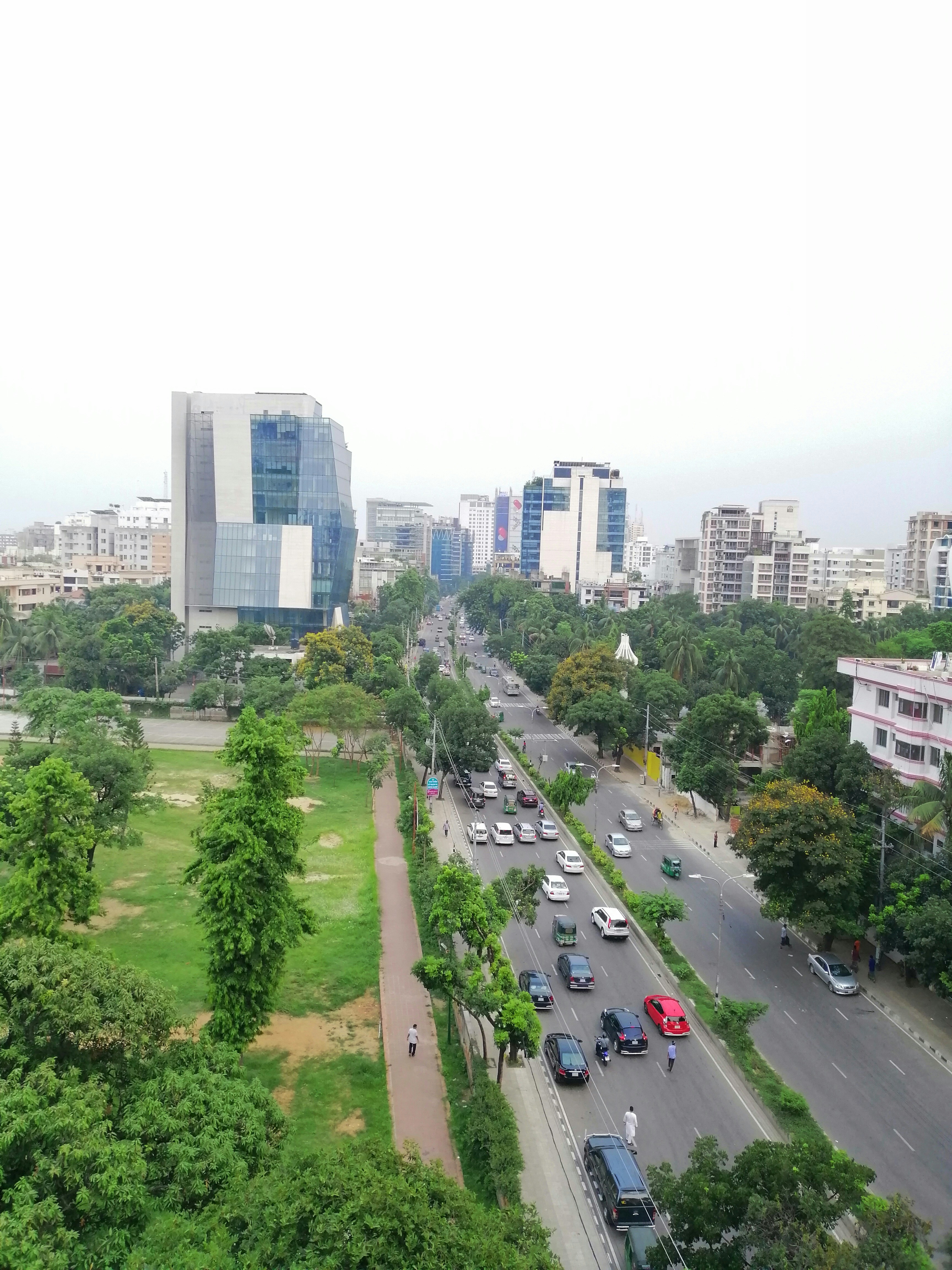 Aerial view of a bustling city road flanked by greenery and modern architecture, showcasing the blend of urban life and nature.