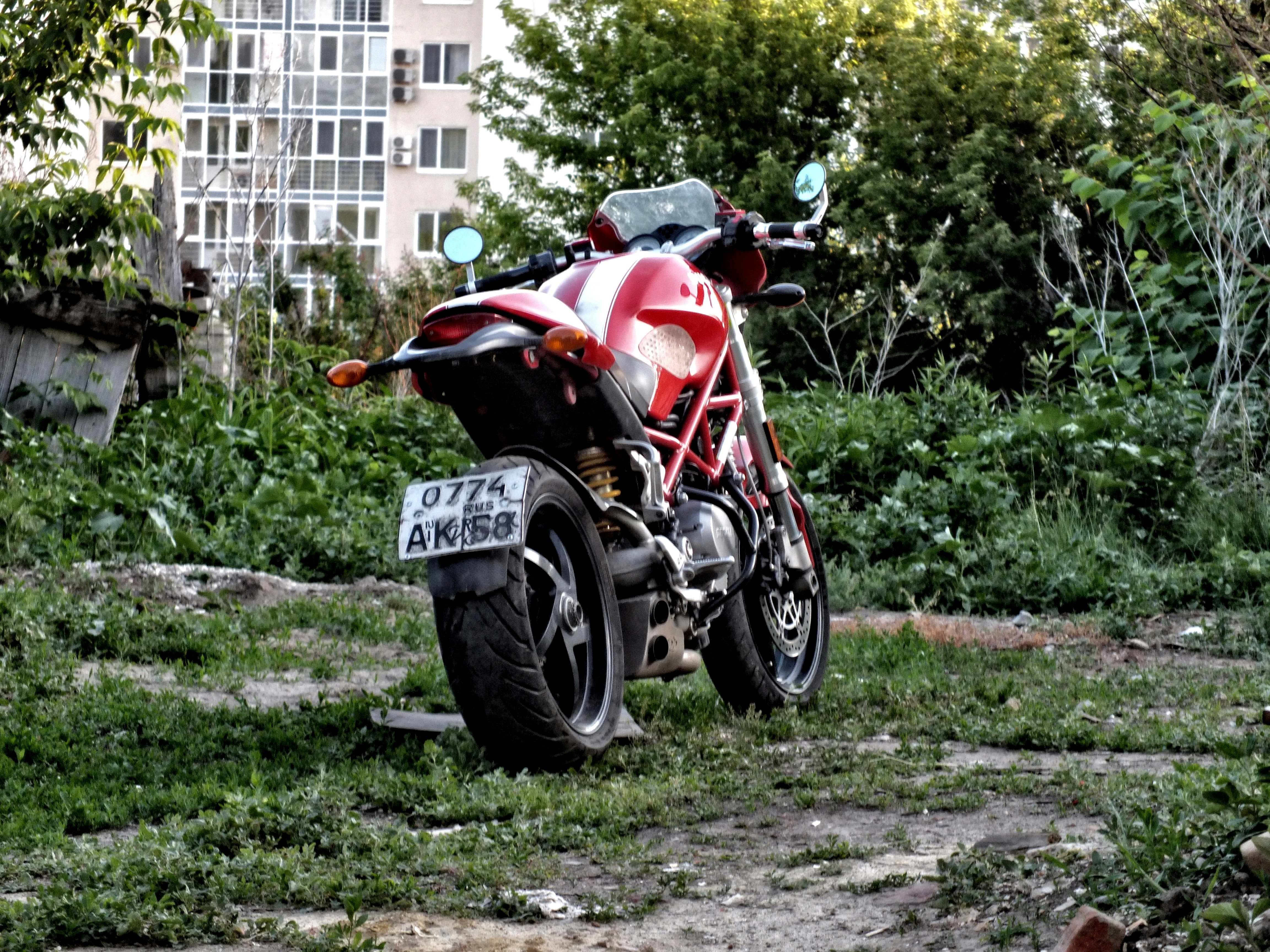 Red Ducati-styled motorcycle rests on a grassy lot amid urban greenery