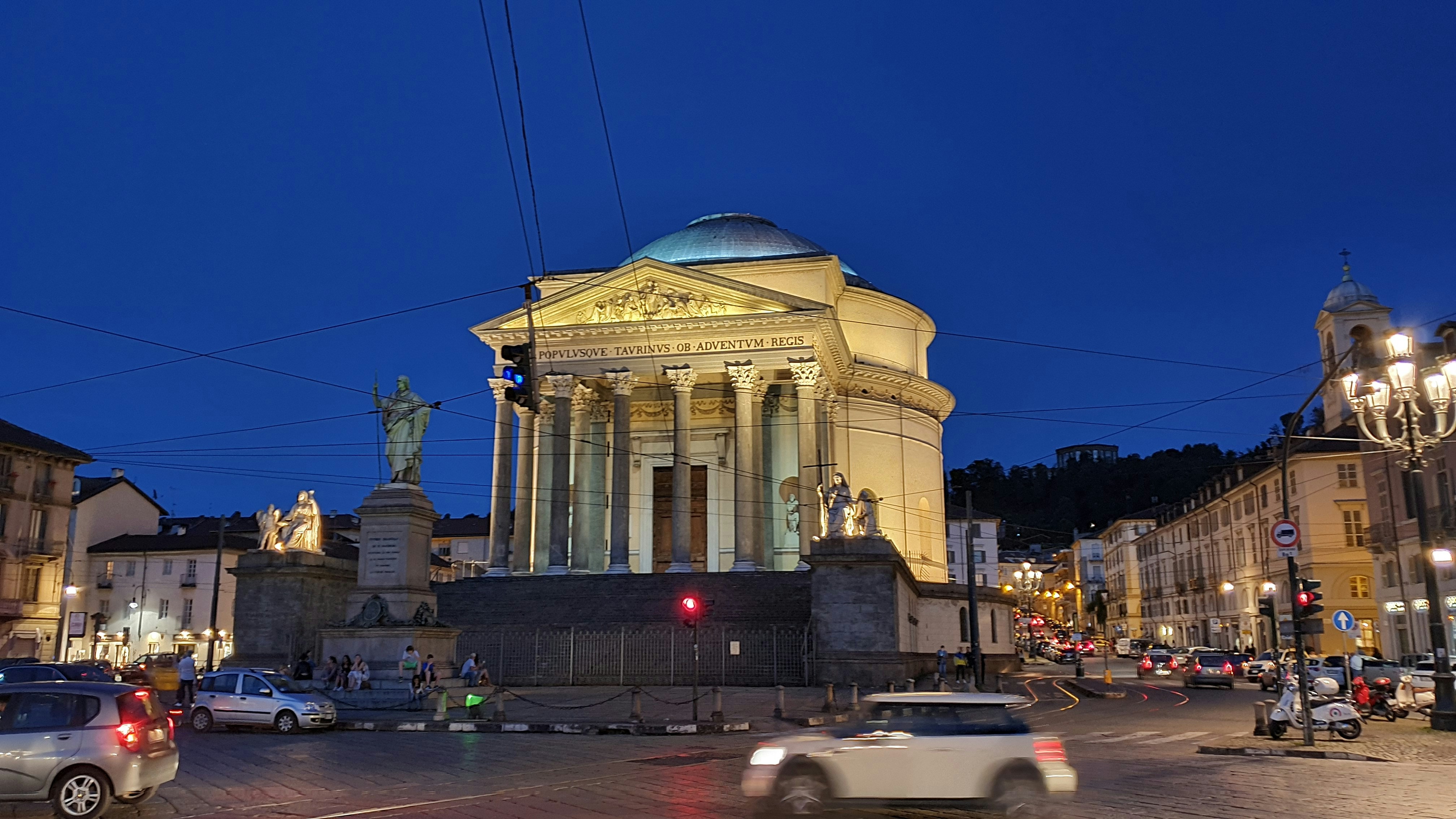 Historic domed building with columns lit against a deep blue evening sky in a bustling city street.