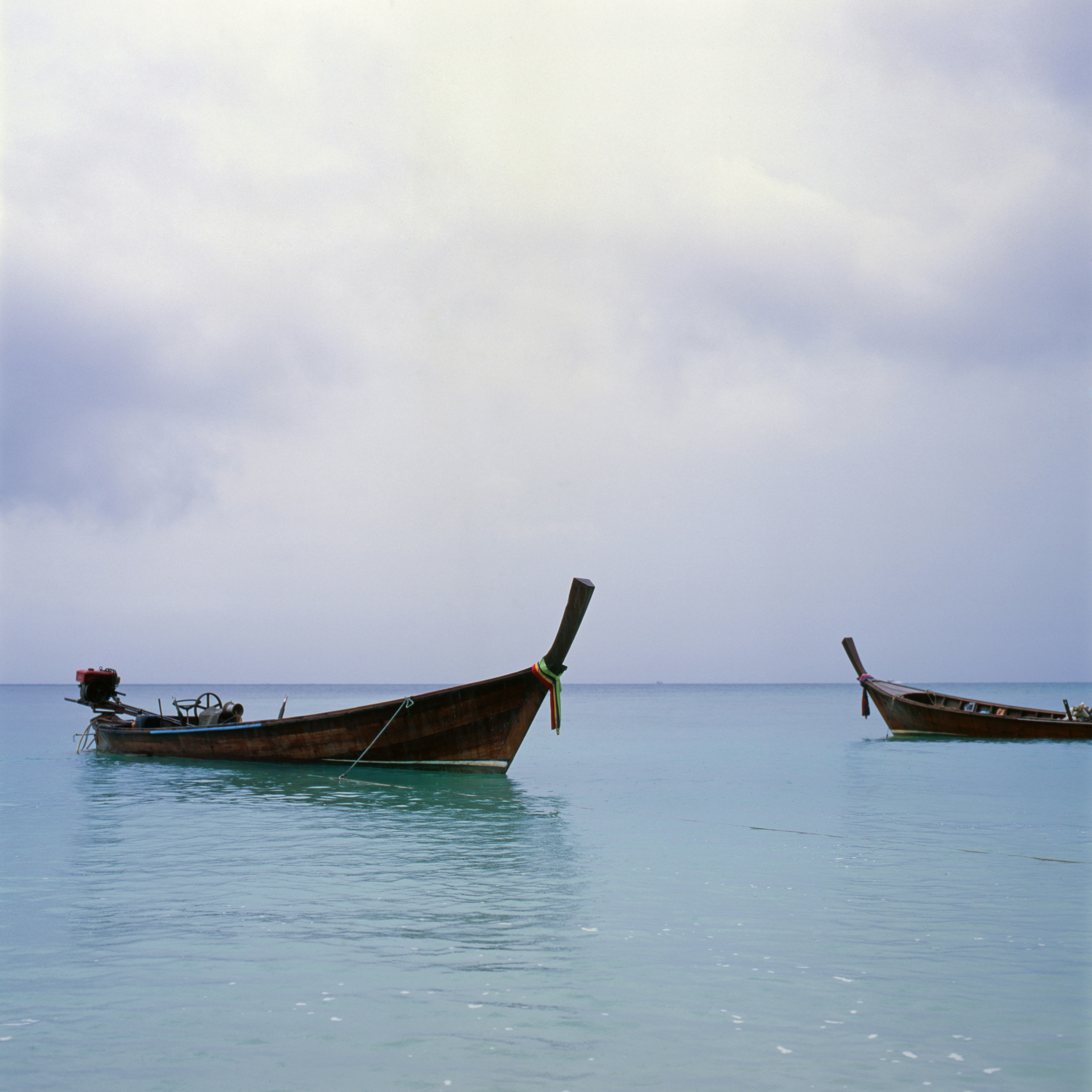 Two traditional boats anchored in calm turquoise waters under a cloudy sky.
