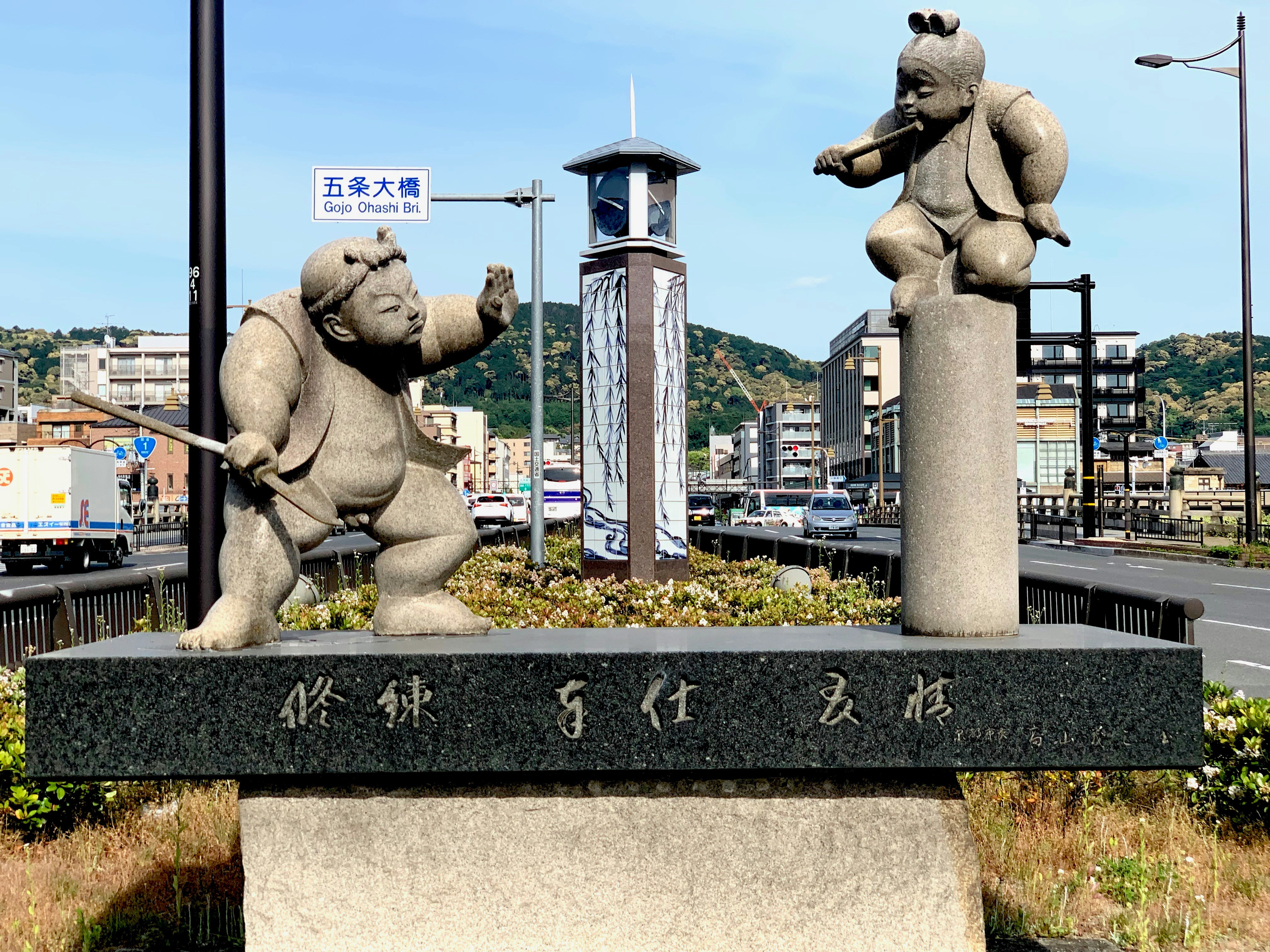 Stone sculptures of two playful figures on a pedestal with urban landscape in the background.