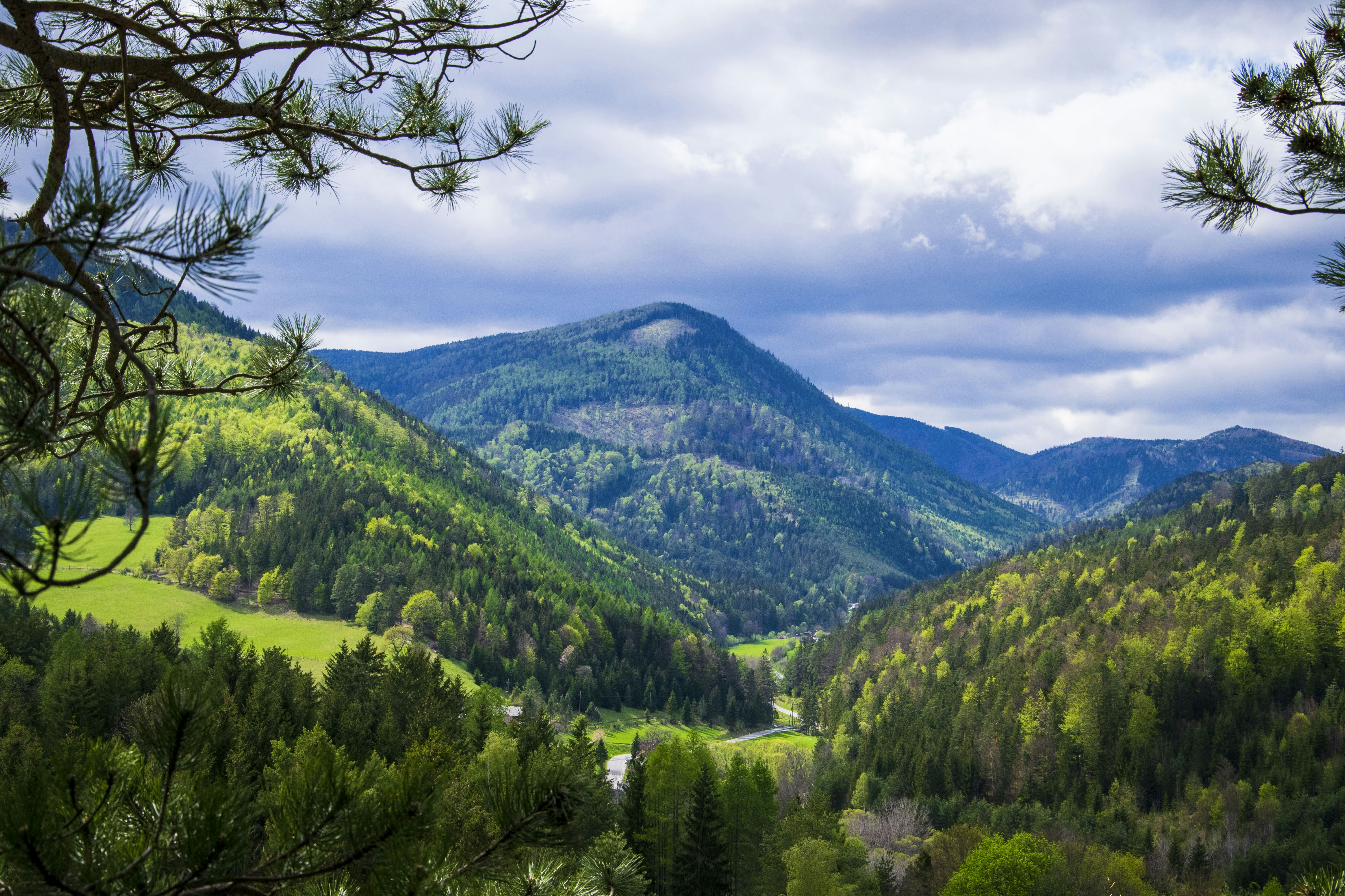 Lush green valleys and forested mountains under a sky filled with dramatic clouds.