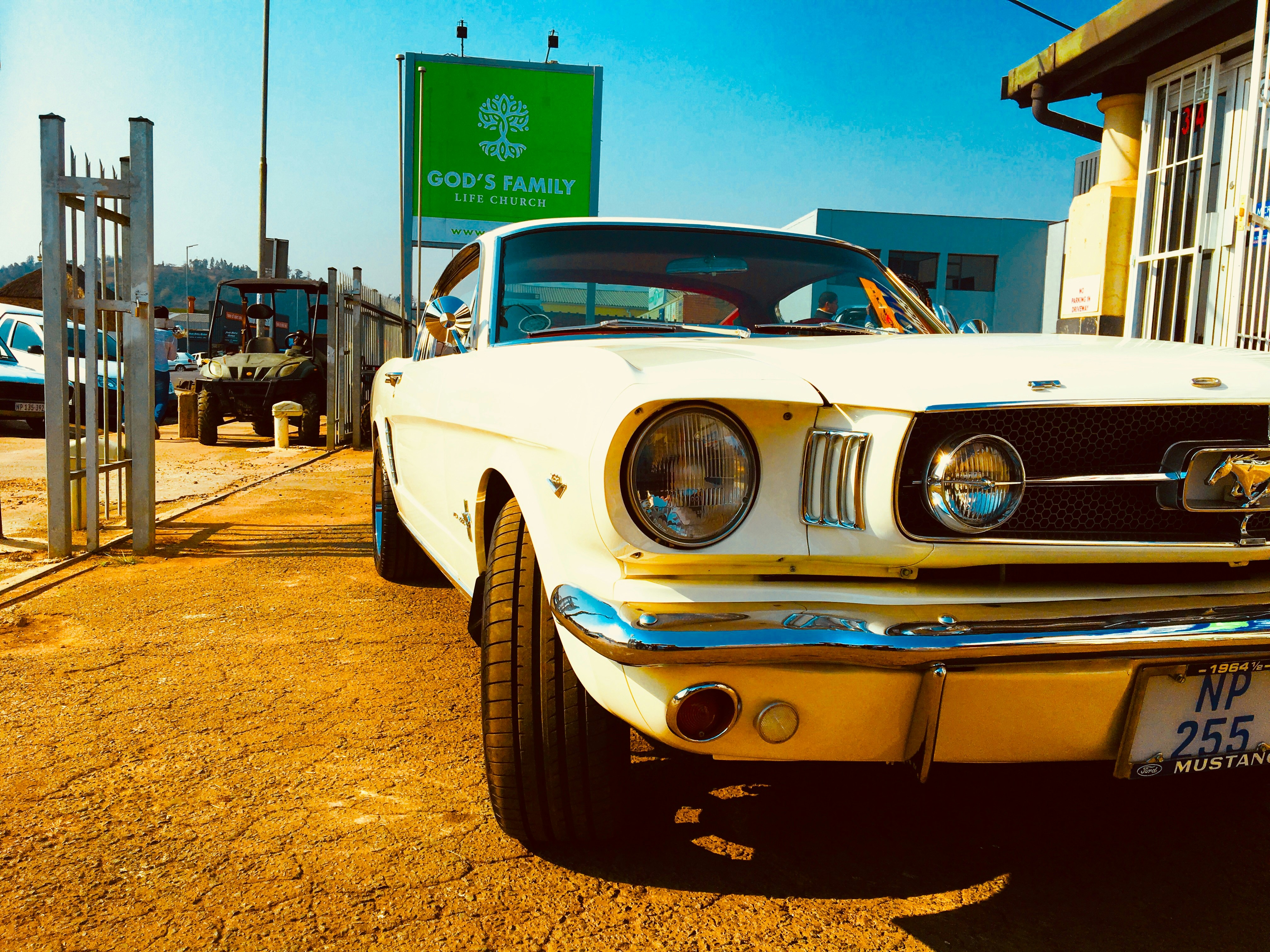 Classic white Ford Mustang parked near a building under a clear blue sky.