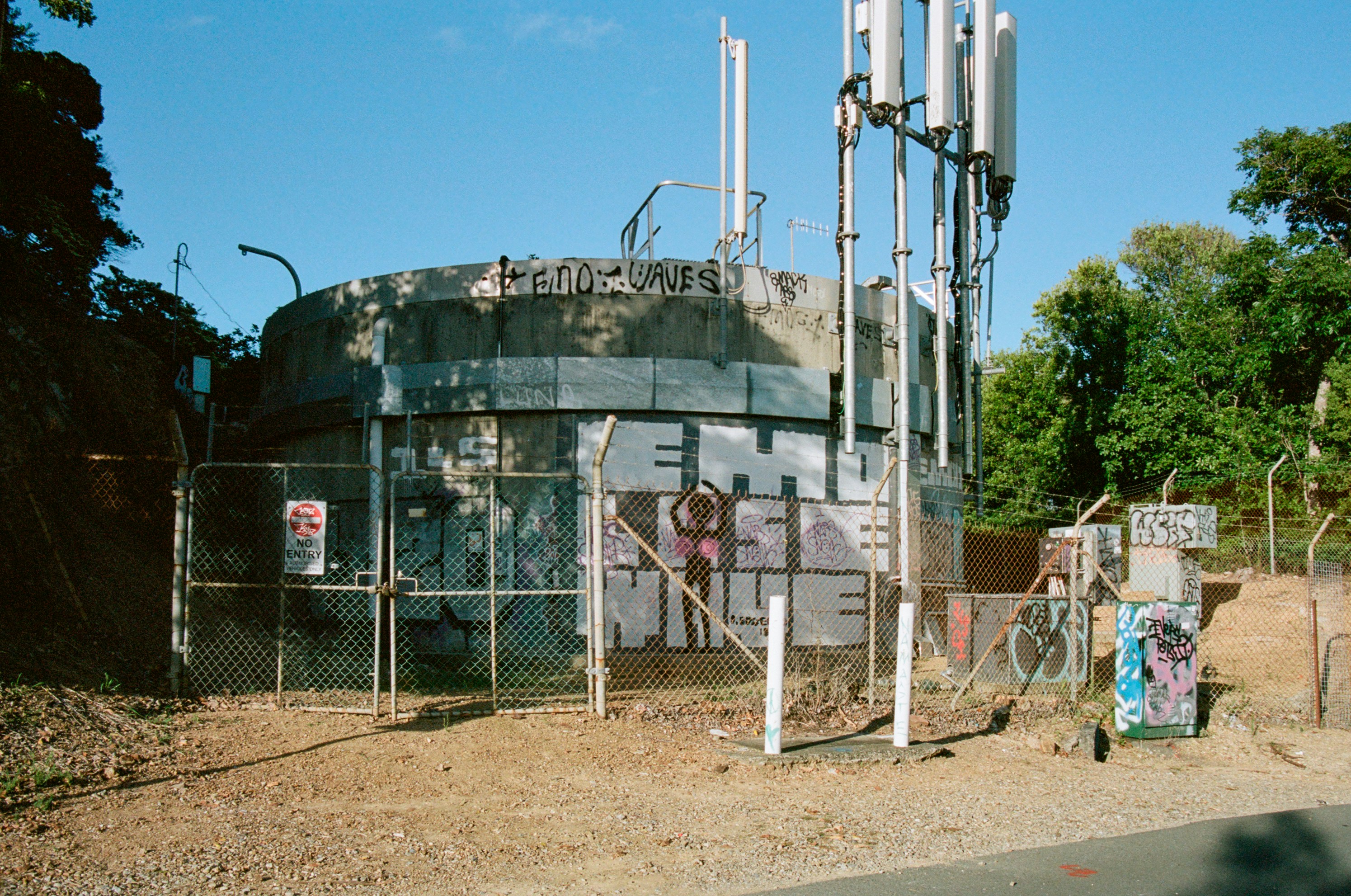 Graffiti-covered water tower surrounded by telecommunications equipment, showcasing the contrast between nature and urban infrastructure.