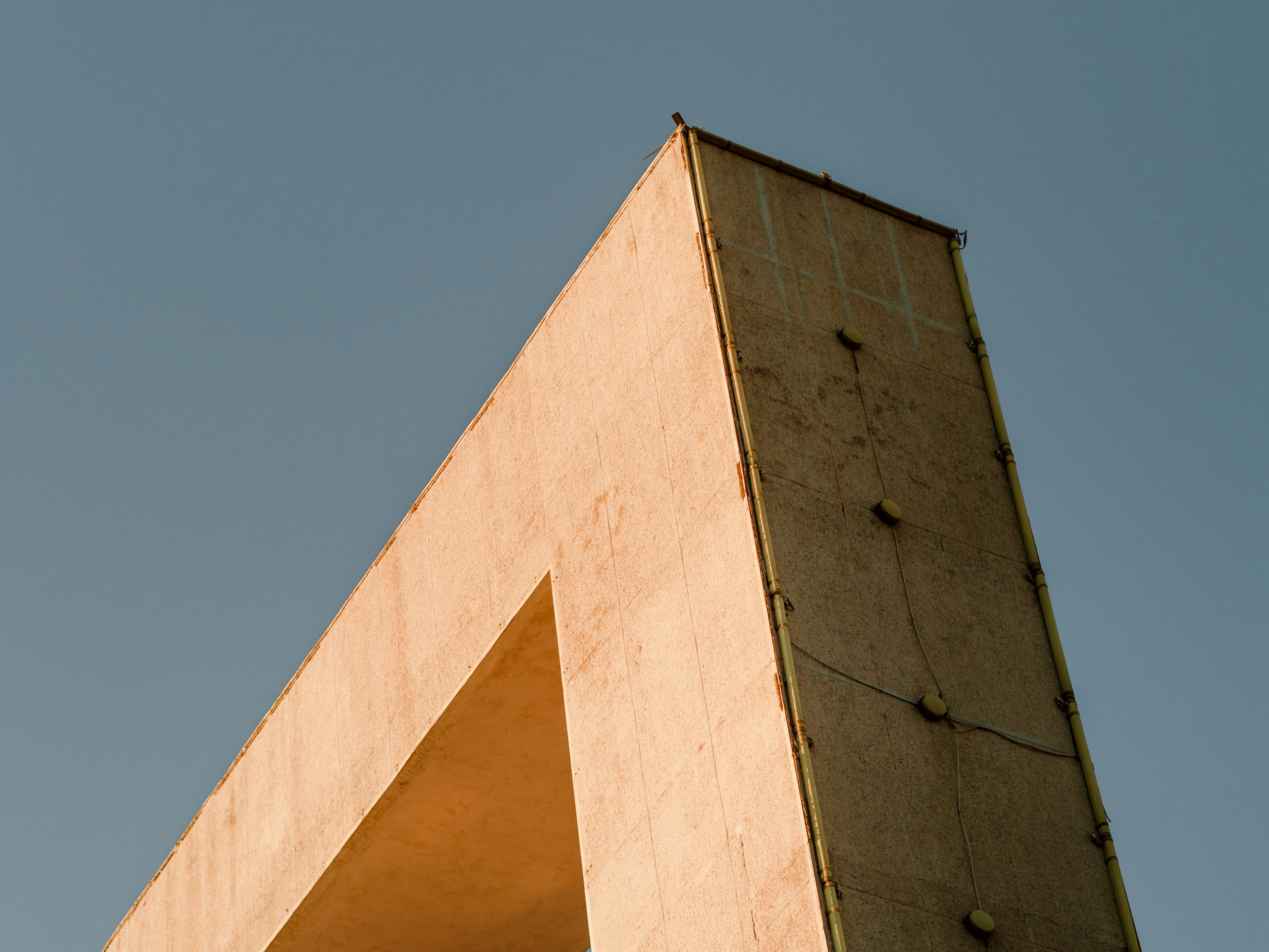 Abstract view of a large concrete structure against a clear blue sky, emphasizing geometric shapes and lines.