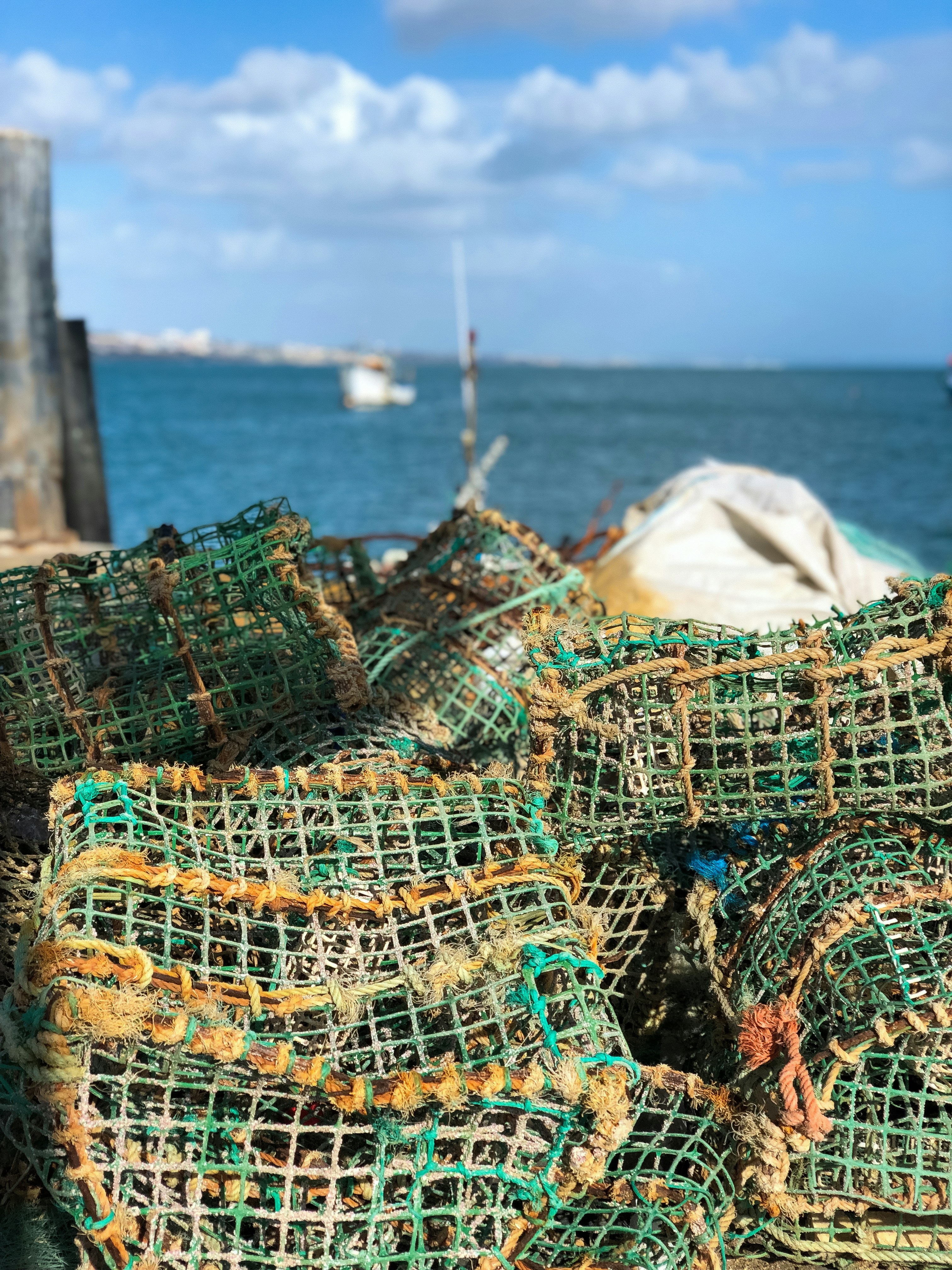 Colorful fishing nets piled on a dock with boats in the background under a bright blue sky.