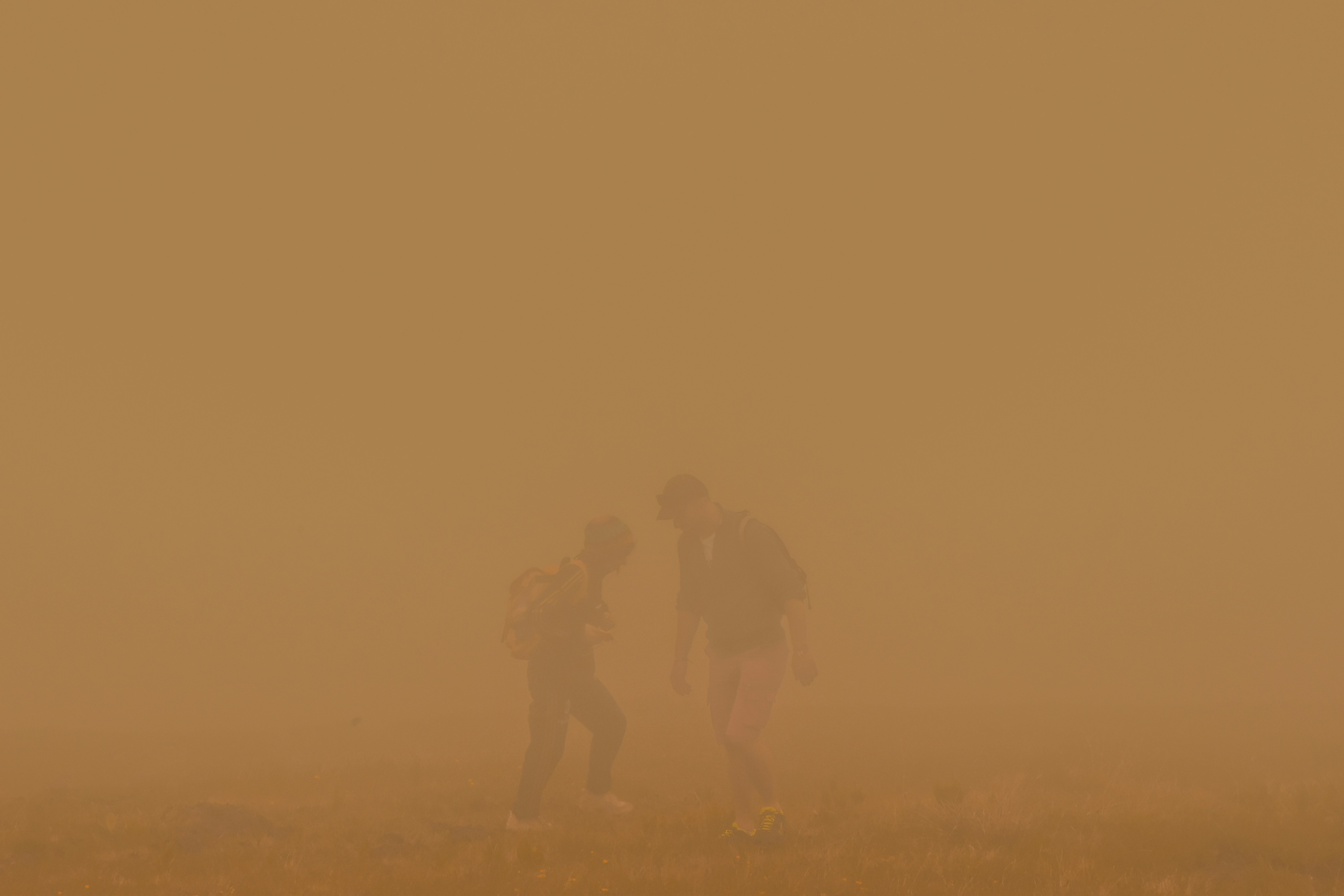 Two people with backpacks walking through a dense orange mist in a grassy field.