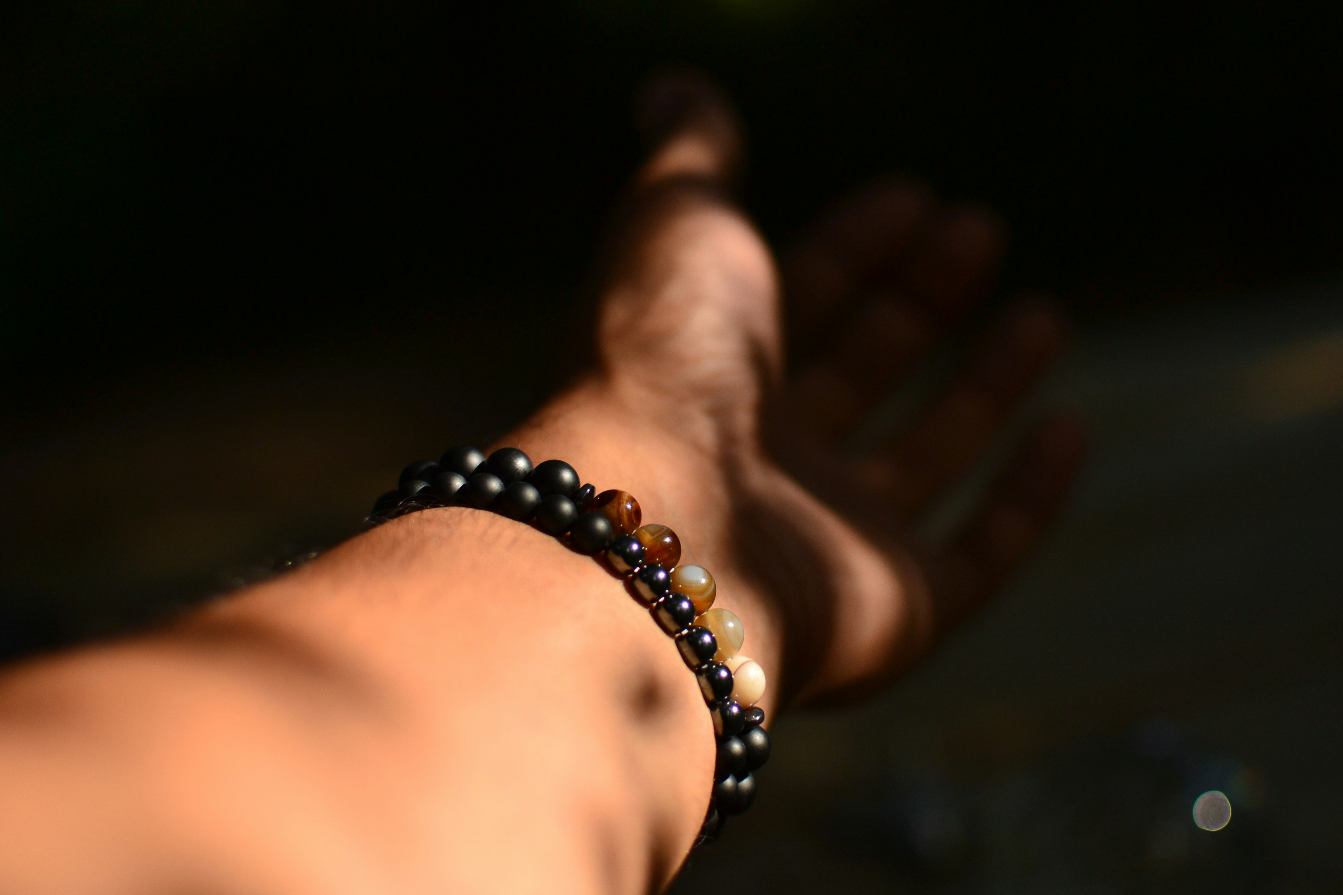 Close-up of a hand adorned with a beaded bracelet, reaching outward against a softly blurred background.