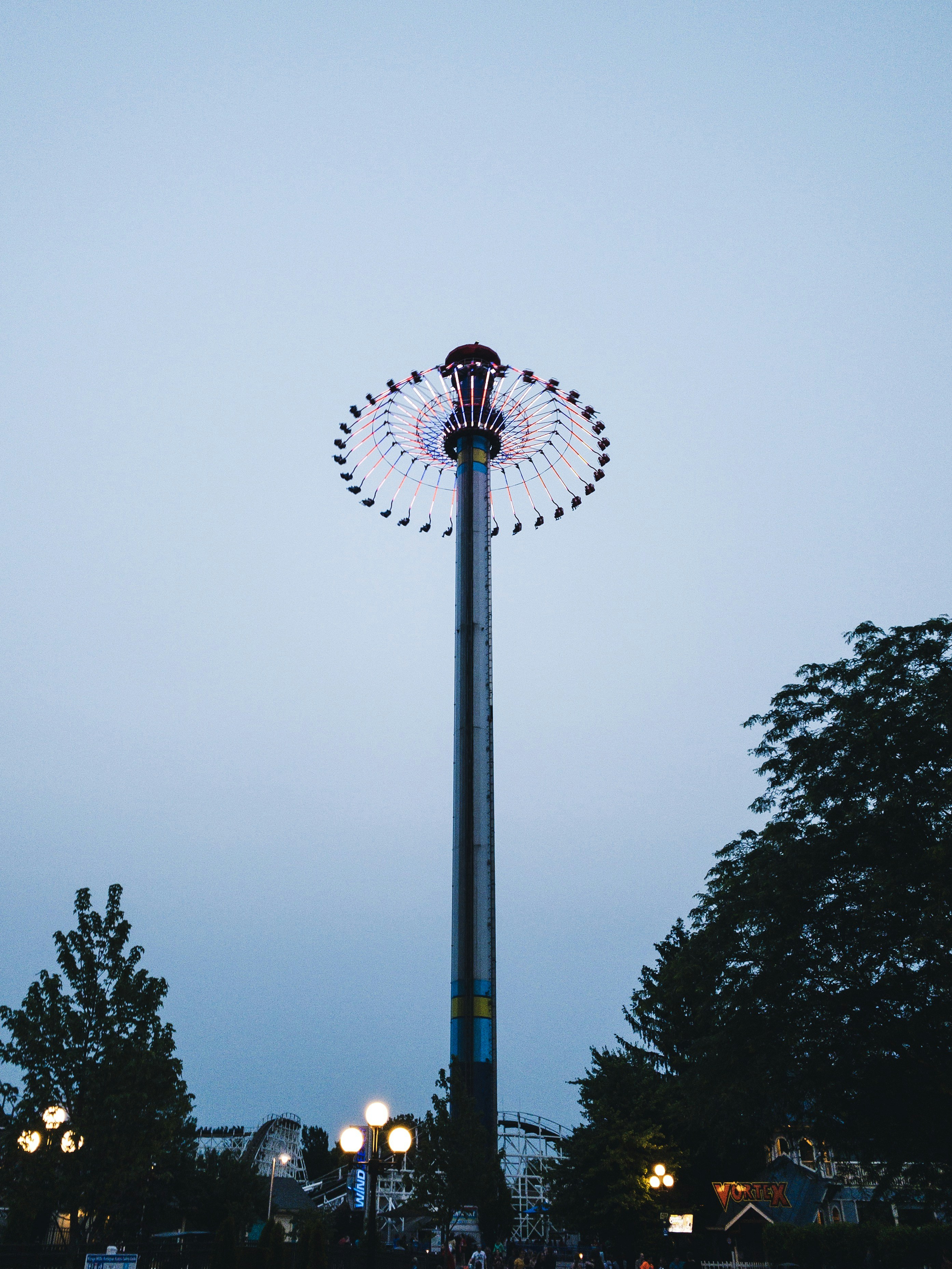 A towering amusement park ride with a circular swing at the top, surrounded by trees and a fading twilight sky.