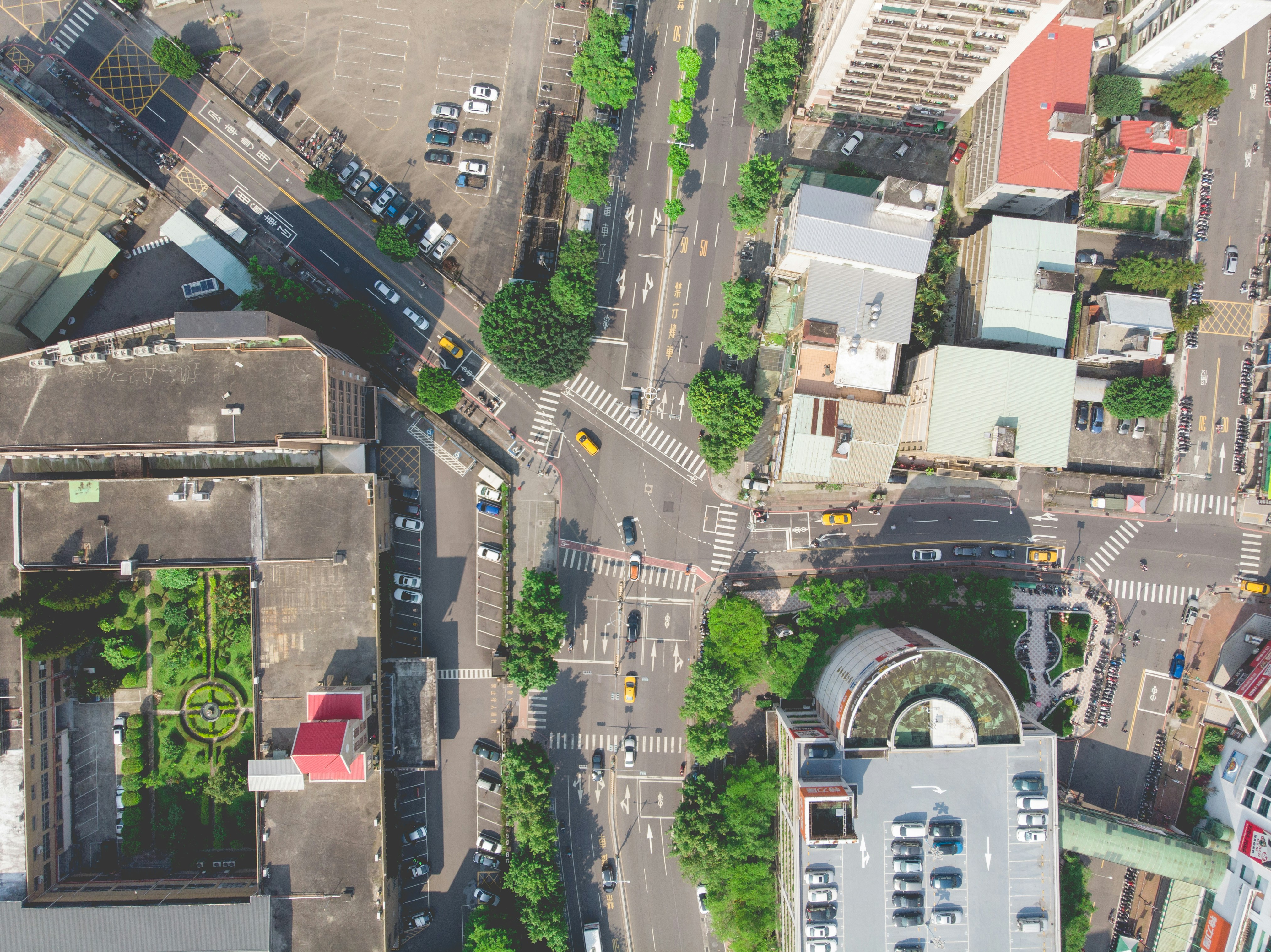 Aerial view of a bustling urban intersection surrounded by greenery and buildings, showcasing the dynamic flow of city life.