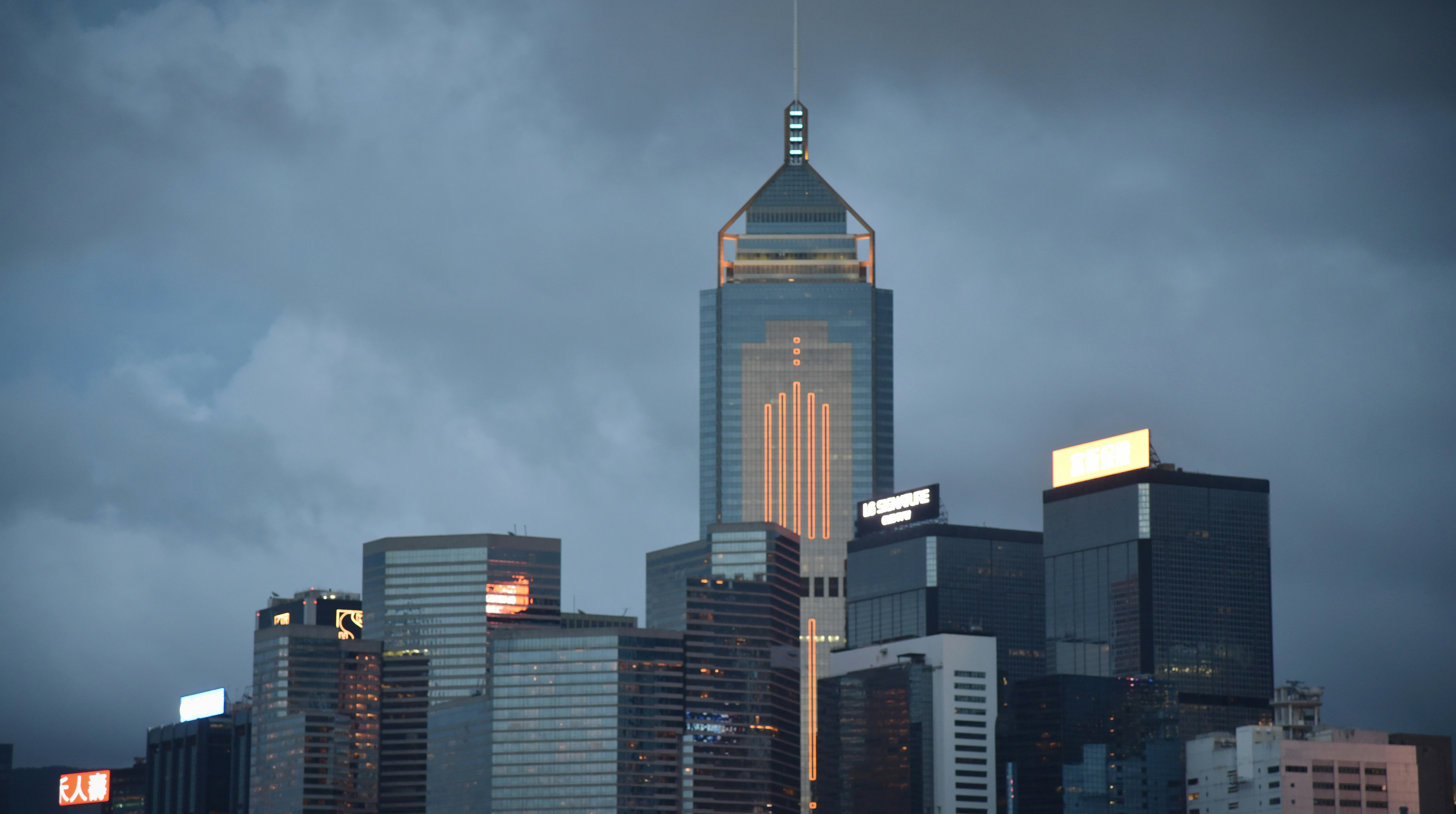 Tall skyscraper with illuminated vertical lines against a backdrop of dark clouds.