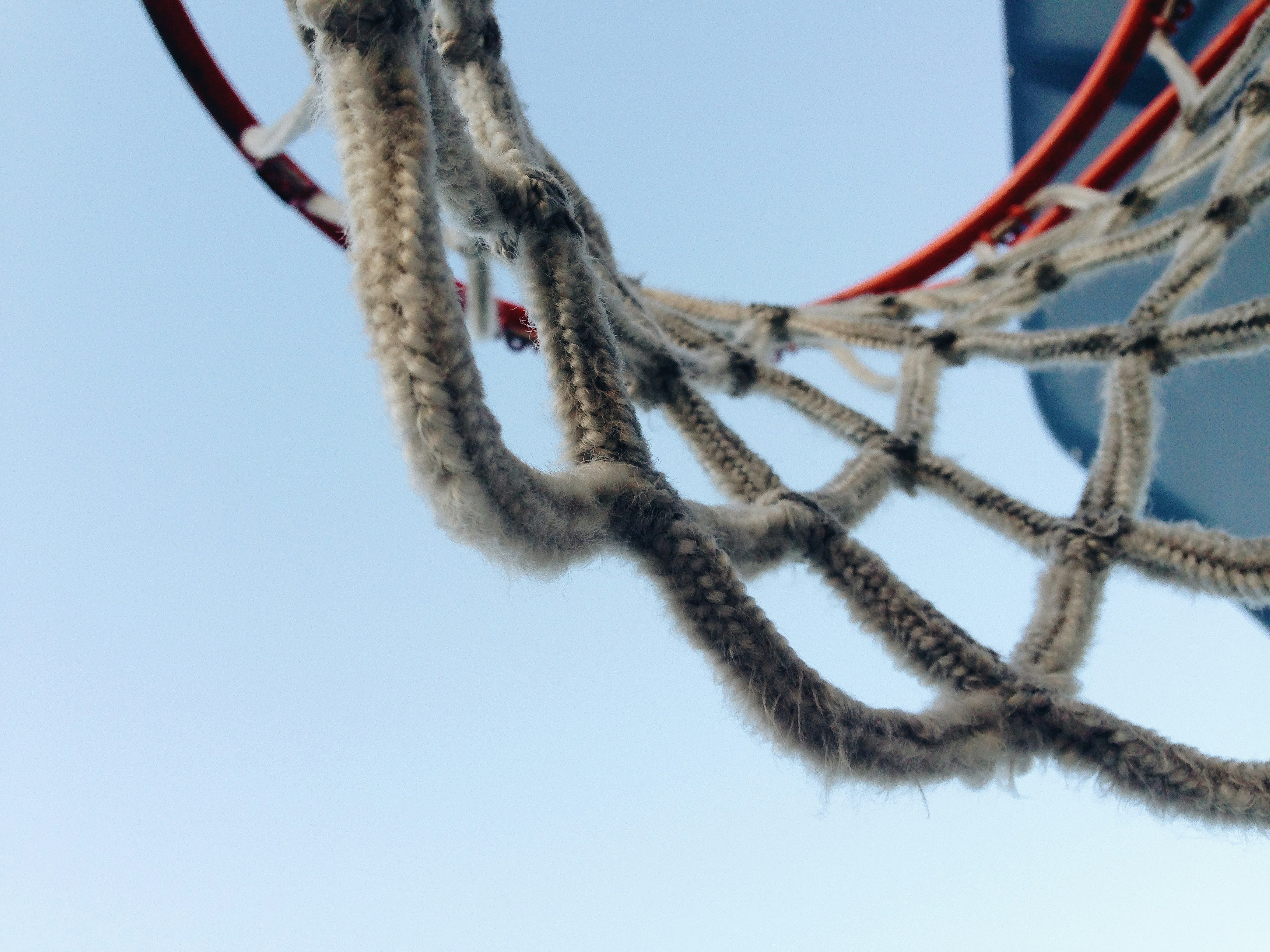Close-up view of a basketball hoop's net against a clear sky, emphasizing the texture and structure of the netting.