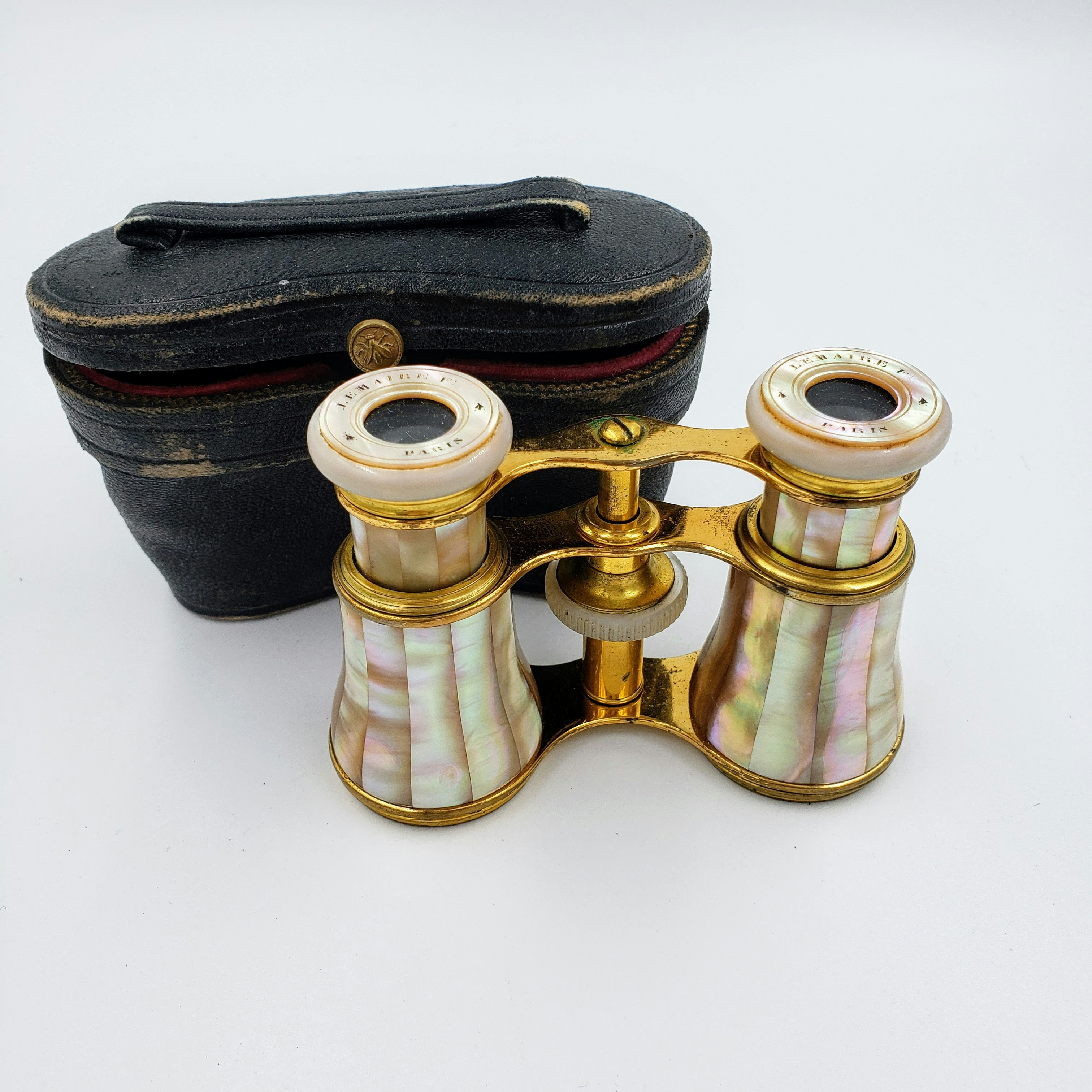 Elegant vintage binoculars with mother-of-pearl inlay resting beside a black leather case.