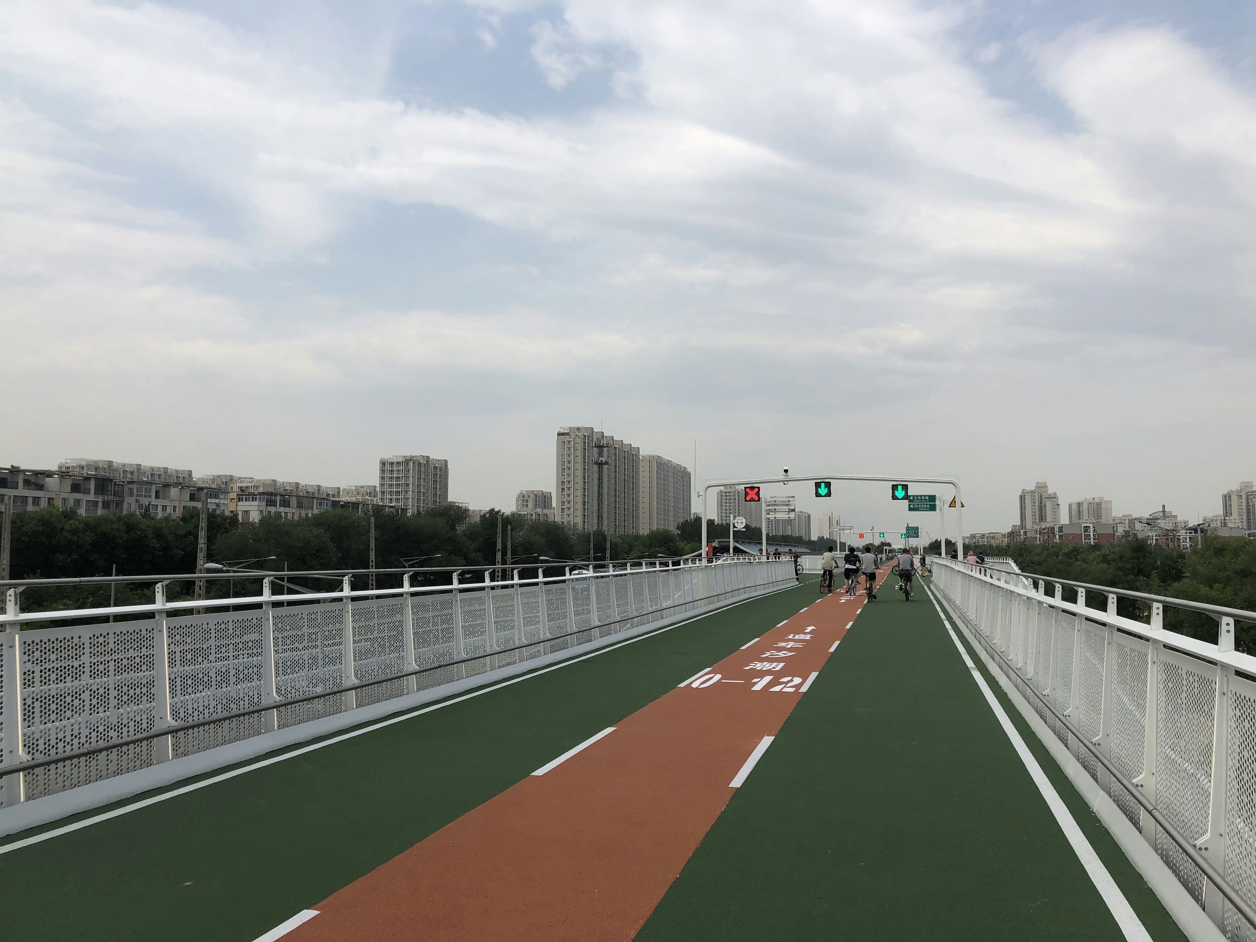 Elevated bicycle highway stretching towards a city skyline under a cloud-dotted sky.