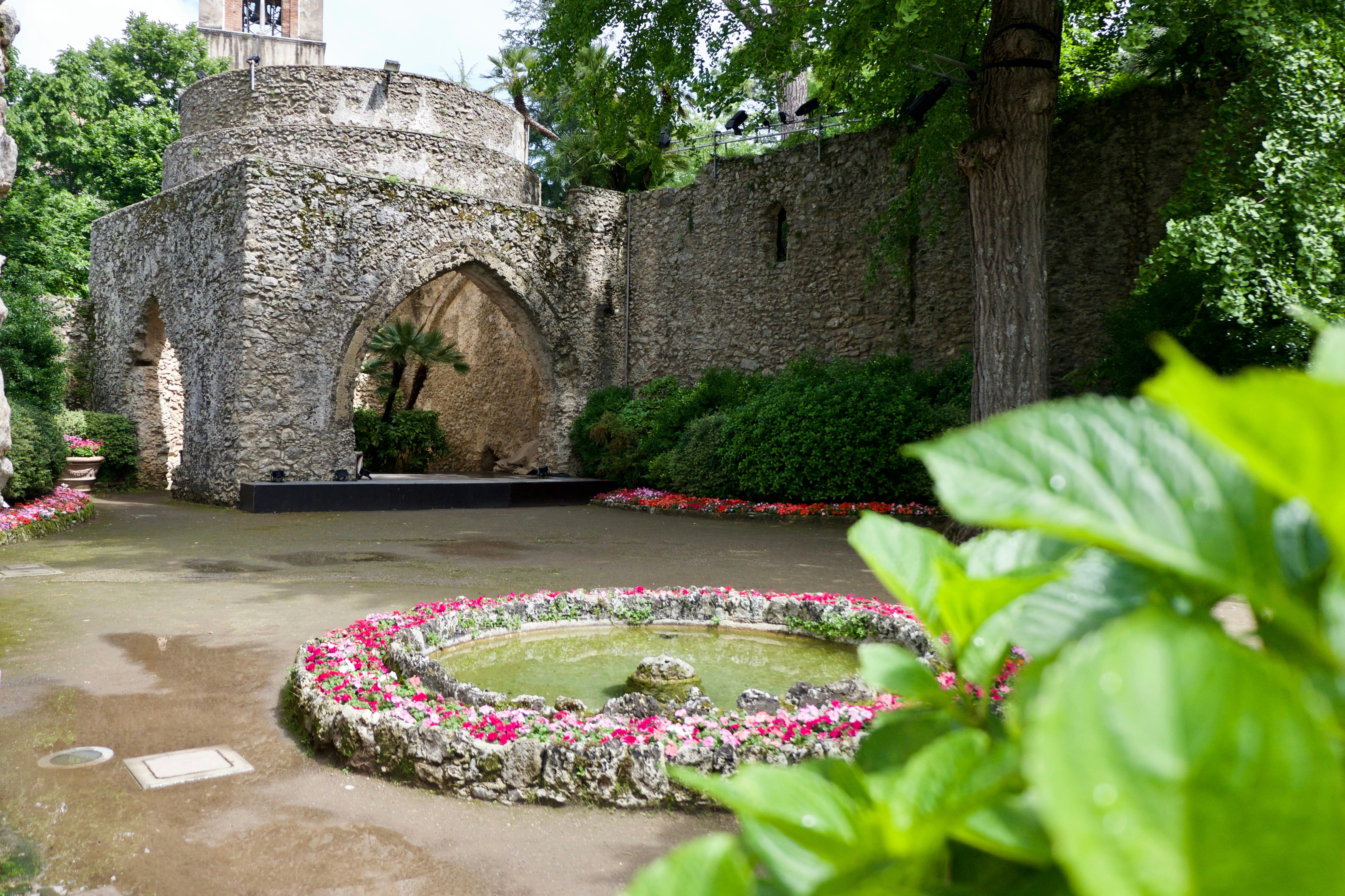 Stone archway and lush garden with circular flower arrangement in a historic setting.