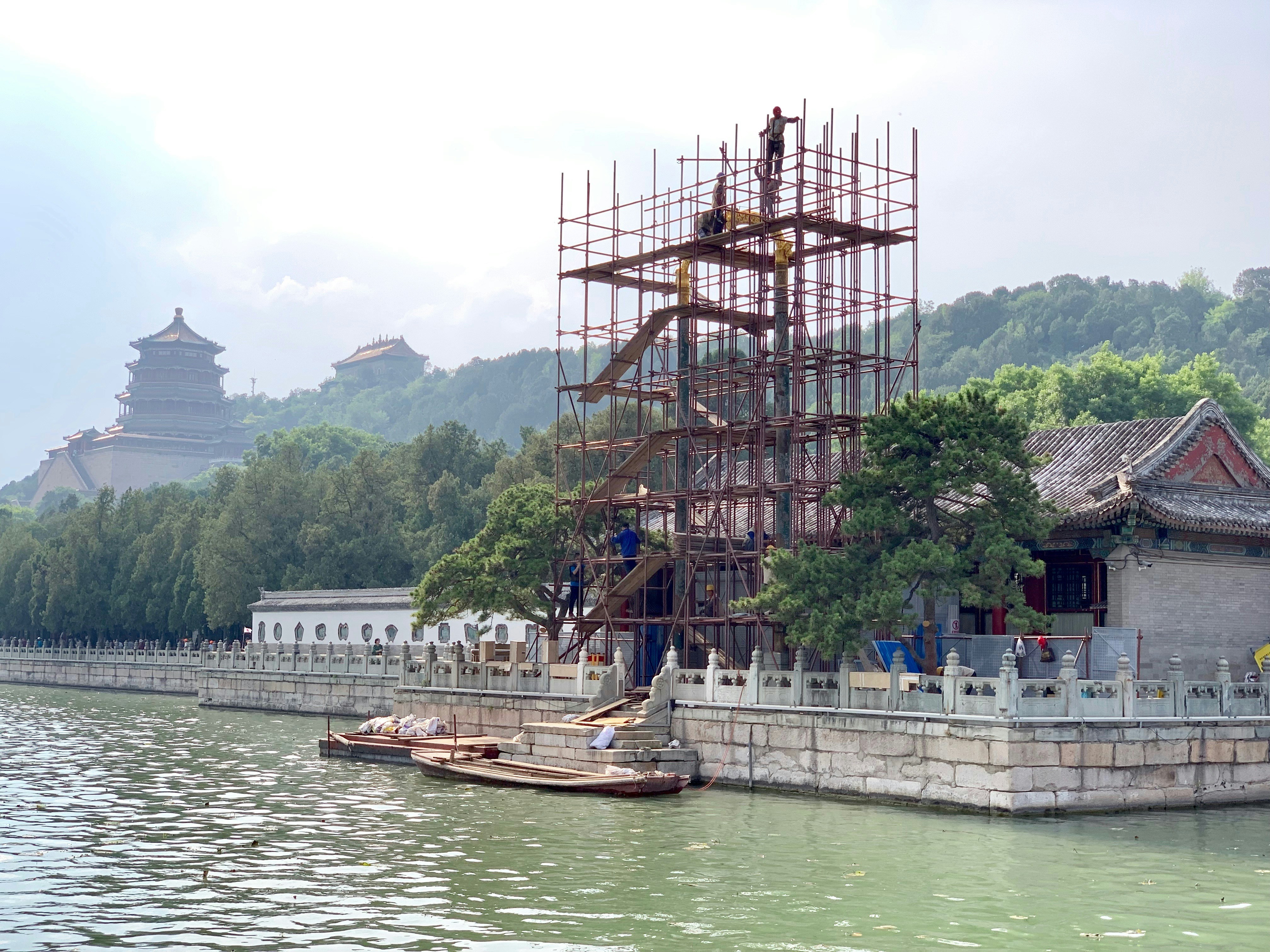 Construction workers on scaffolding at a historical site near a serene lake, showcasing the blend of tradition and restoration efforts.