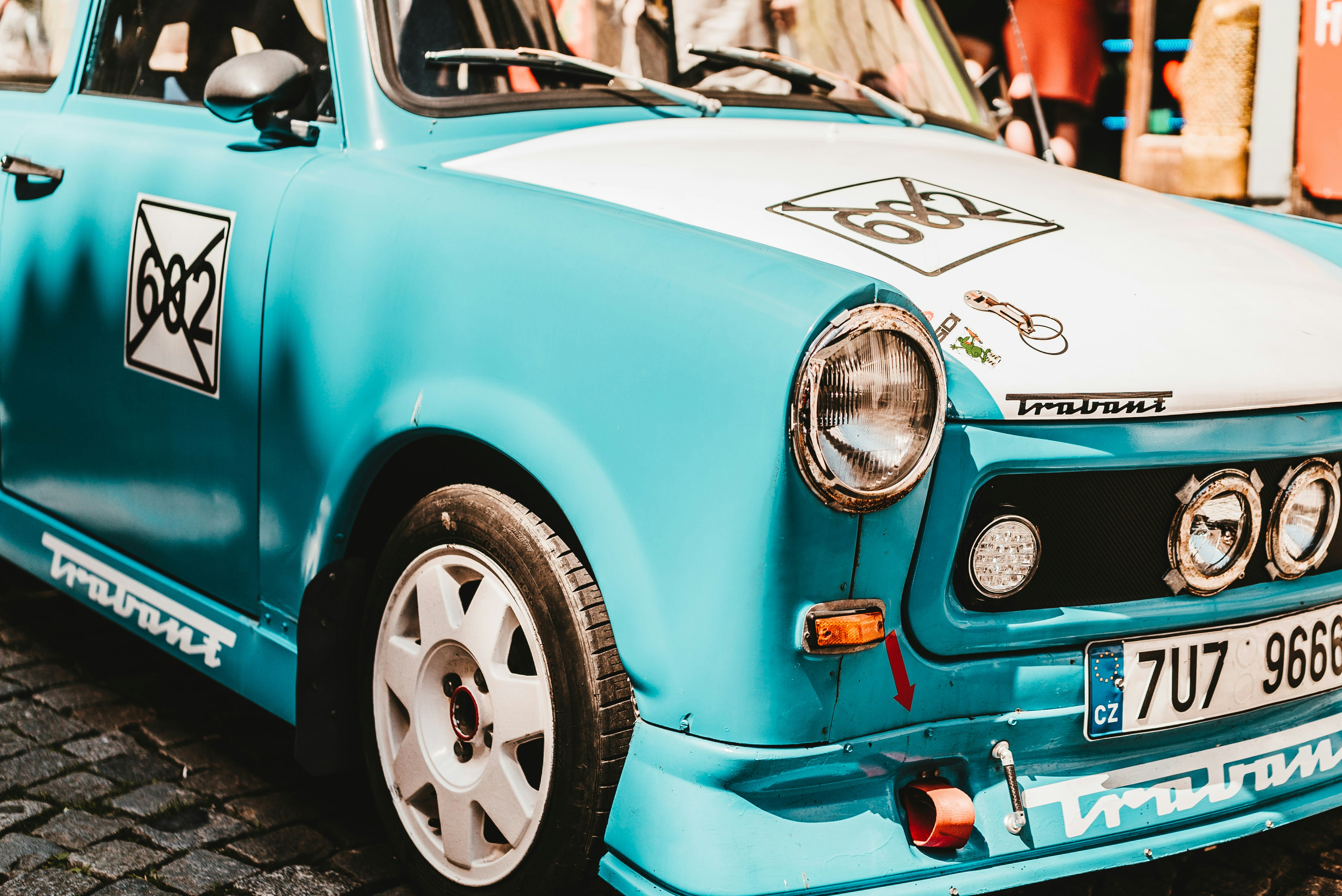 Vibrantly colored Trabant car parked on cobblestone street, showcasing its unique design and vintage racing number. The scene captures the essence of retro automotive culture.
