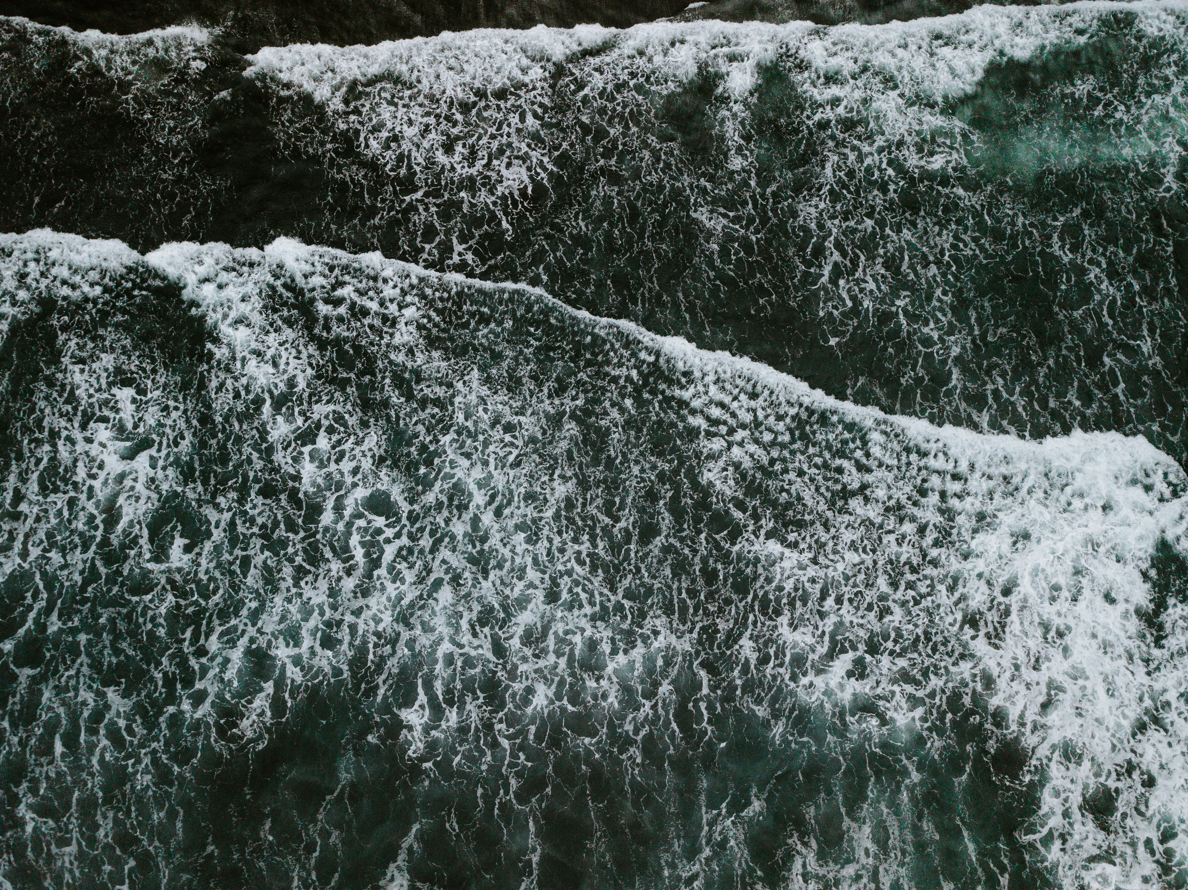 Aerial view of turbulent ocean waves creating intricate patterns as they crash and recede. The dynamic interplay of water showcases the ocean's energy.