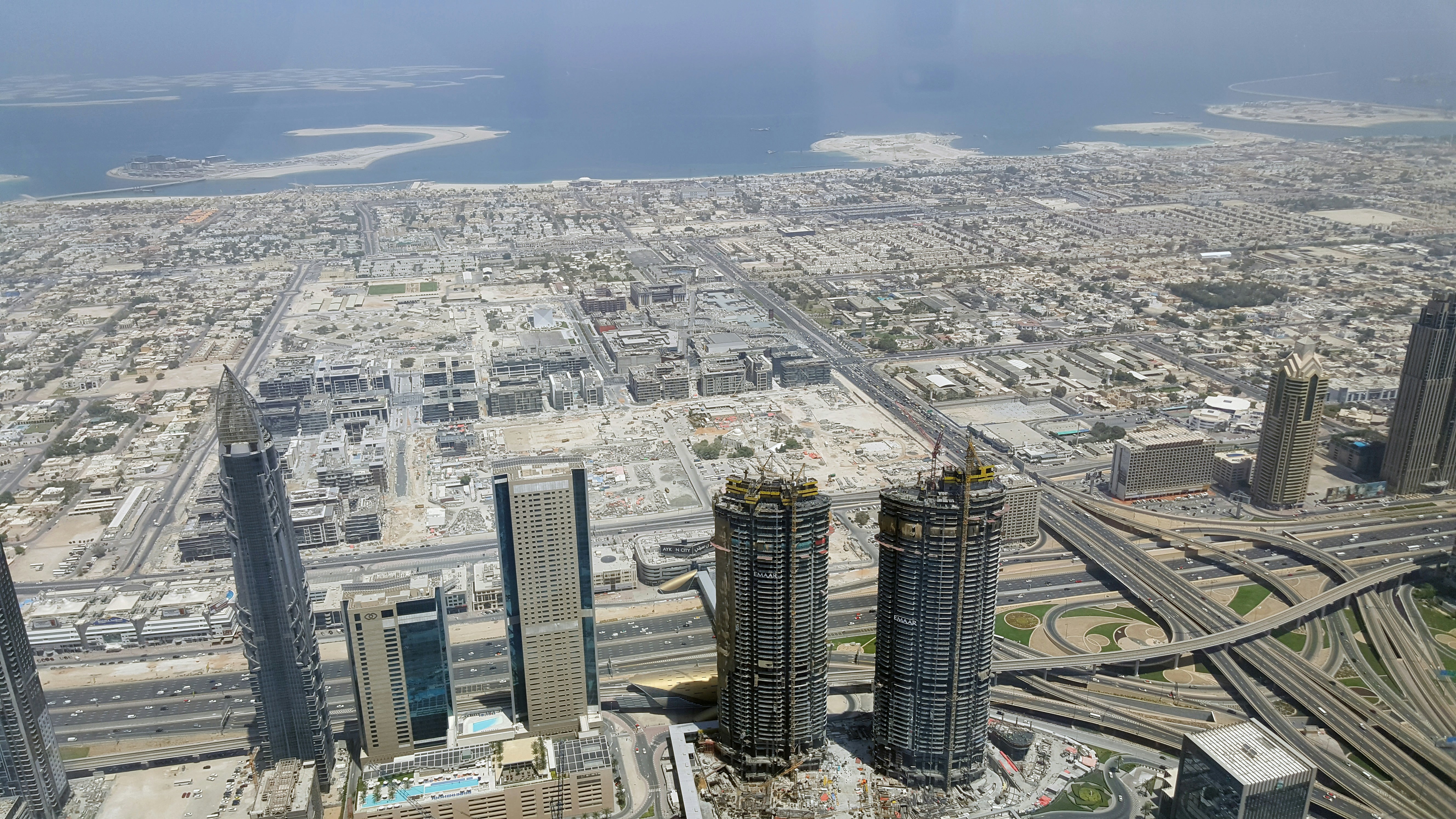 Aerial view showcasing the intricate layout of Dubai's urban development, with high-rise buildings and expansive road networks beneath a clear blue sky.