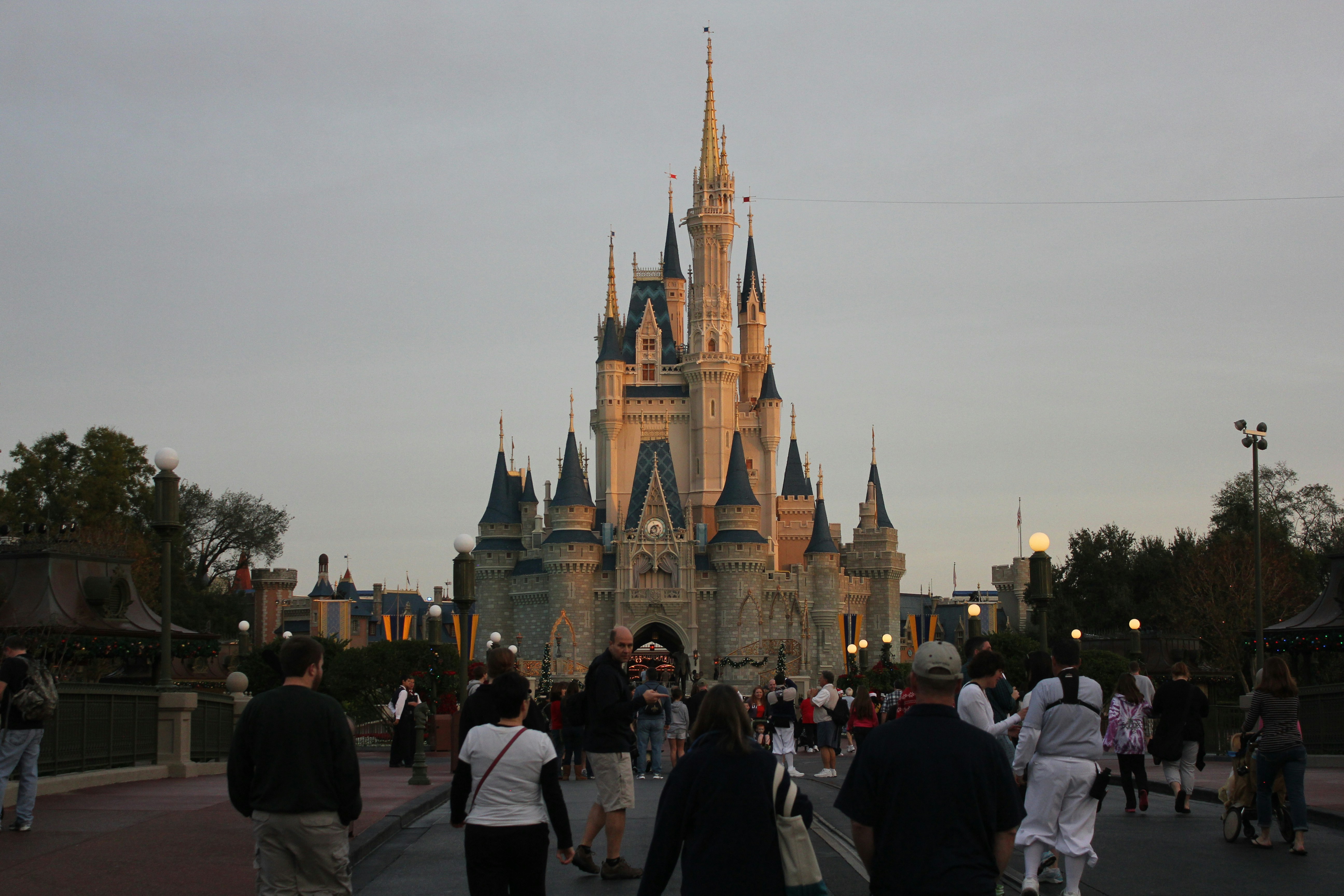 Visitors walking towards a majestic fairytale castle at dusk, surrounded by trees and soft lighting.