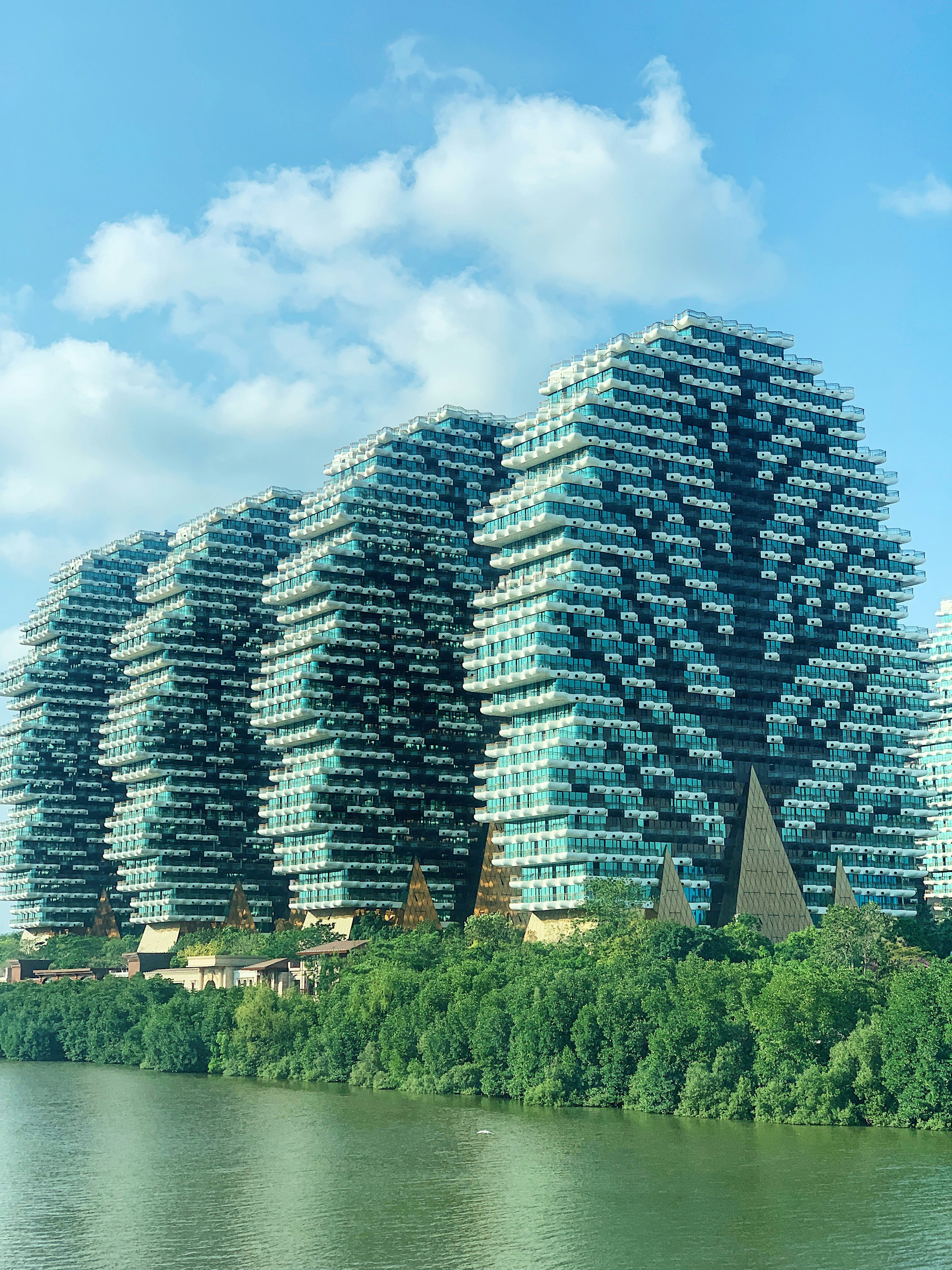 Innovative residential buildings with a unique zigzag structure rise above lush greenery along the water's edge.