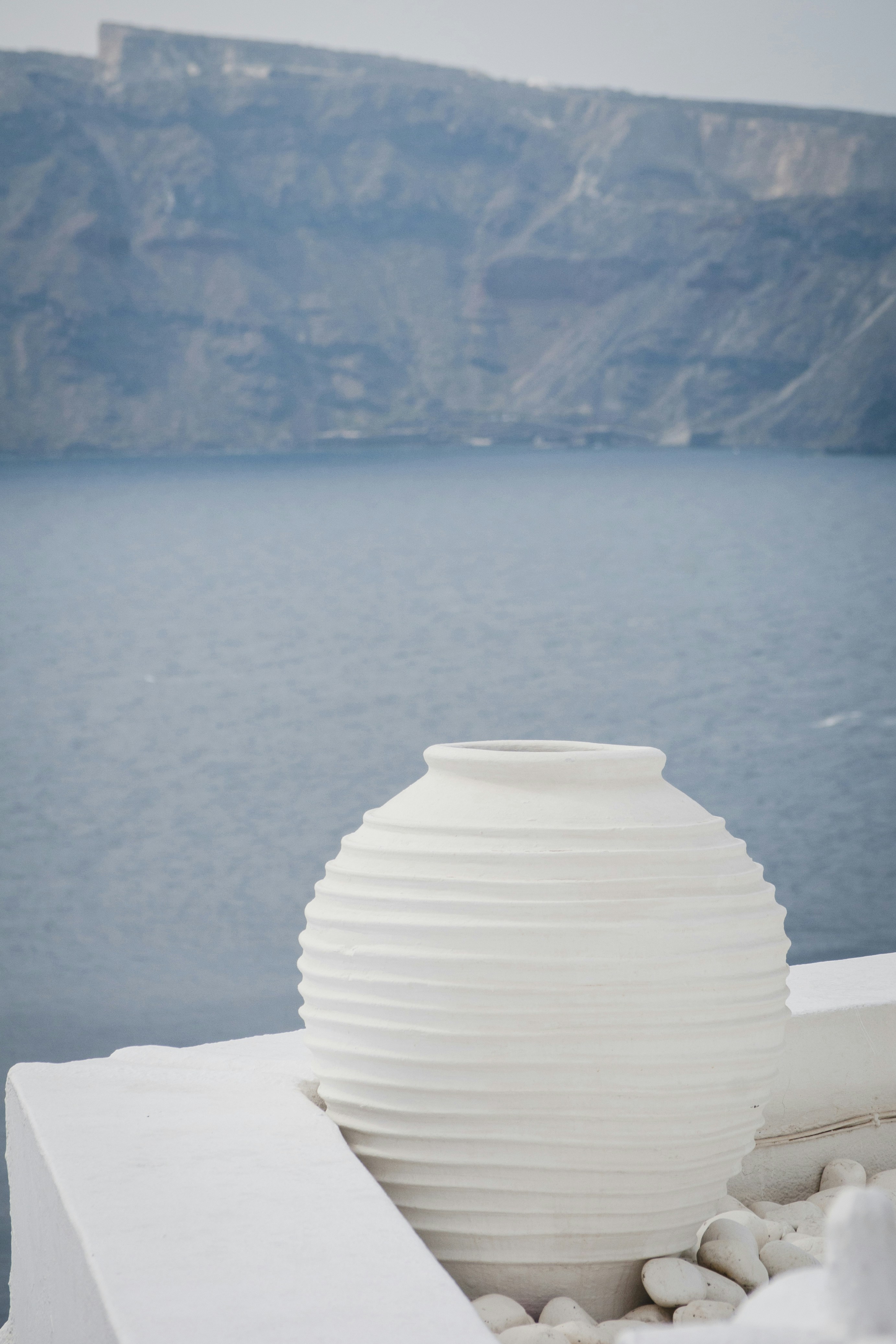 Textured white vase resting on a ledge, overlooking a tranquil sea and distant cliffs.
