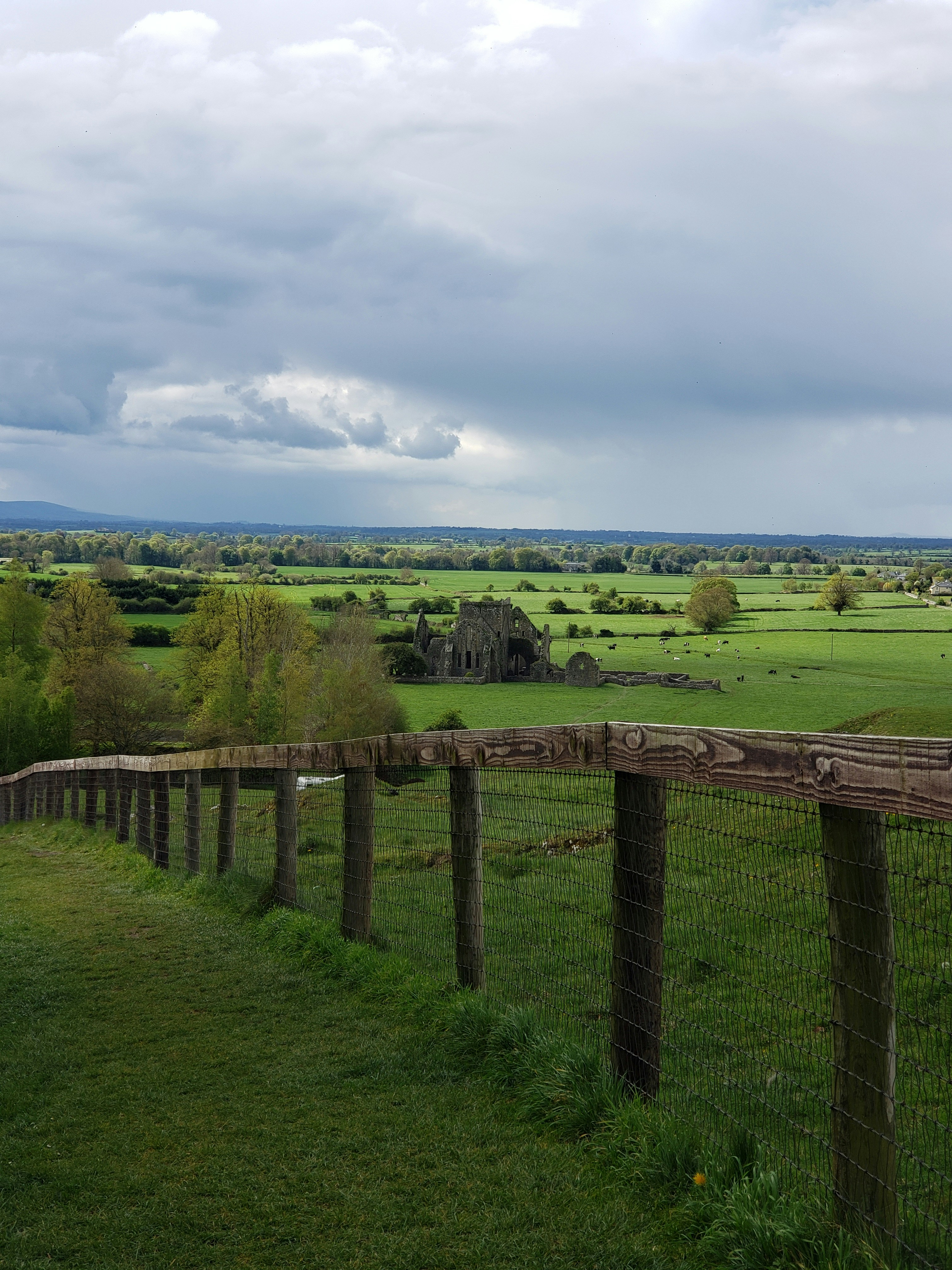 Ruins of an ancient structure nestled in lush green fields under a dramatic sky, showcasing the serene beauty of the countryside.