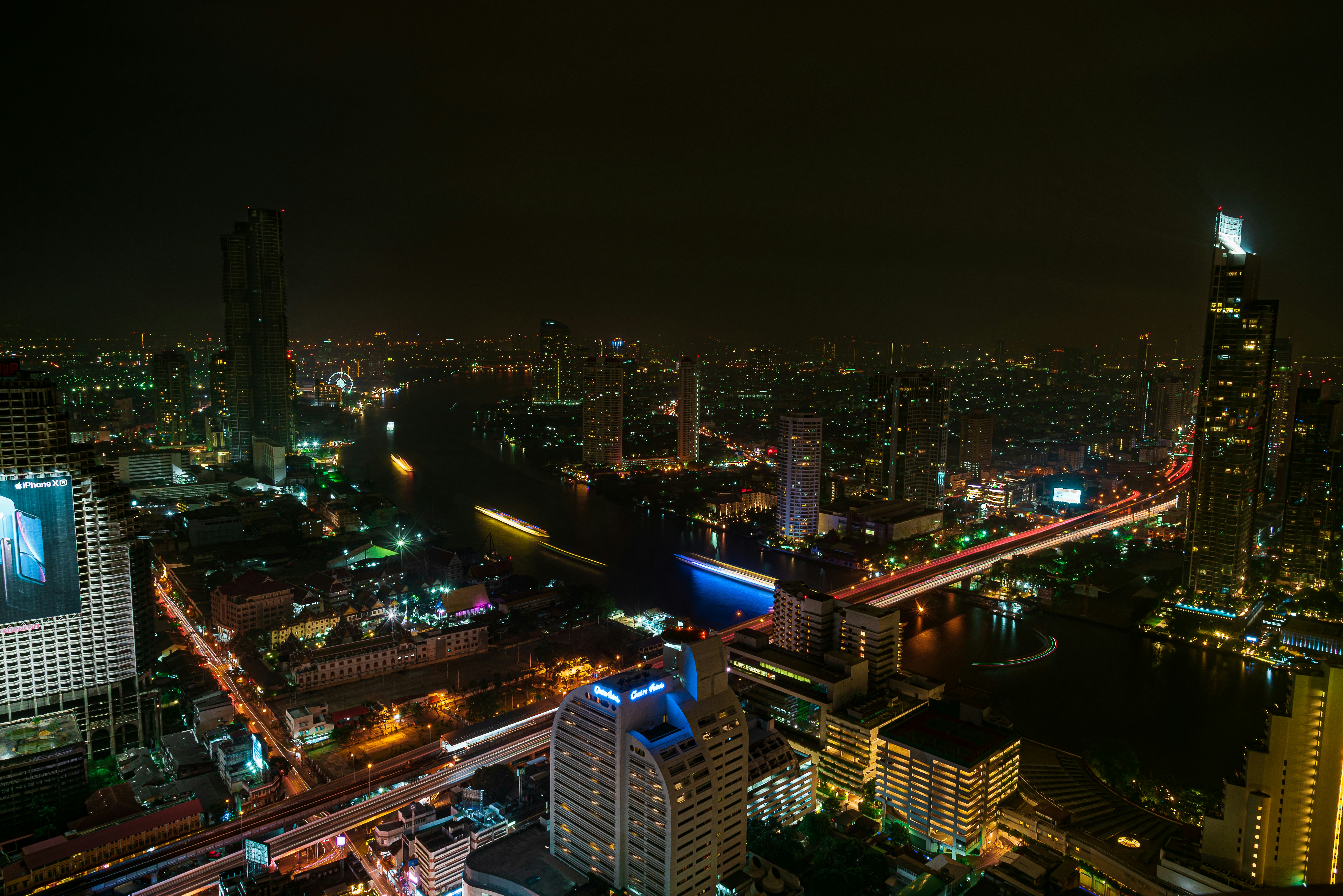 Vibrant cityscape at night showcasing the illuminated skyline of Bangkok with the Chao Phraya River reflecting lights.