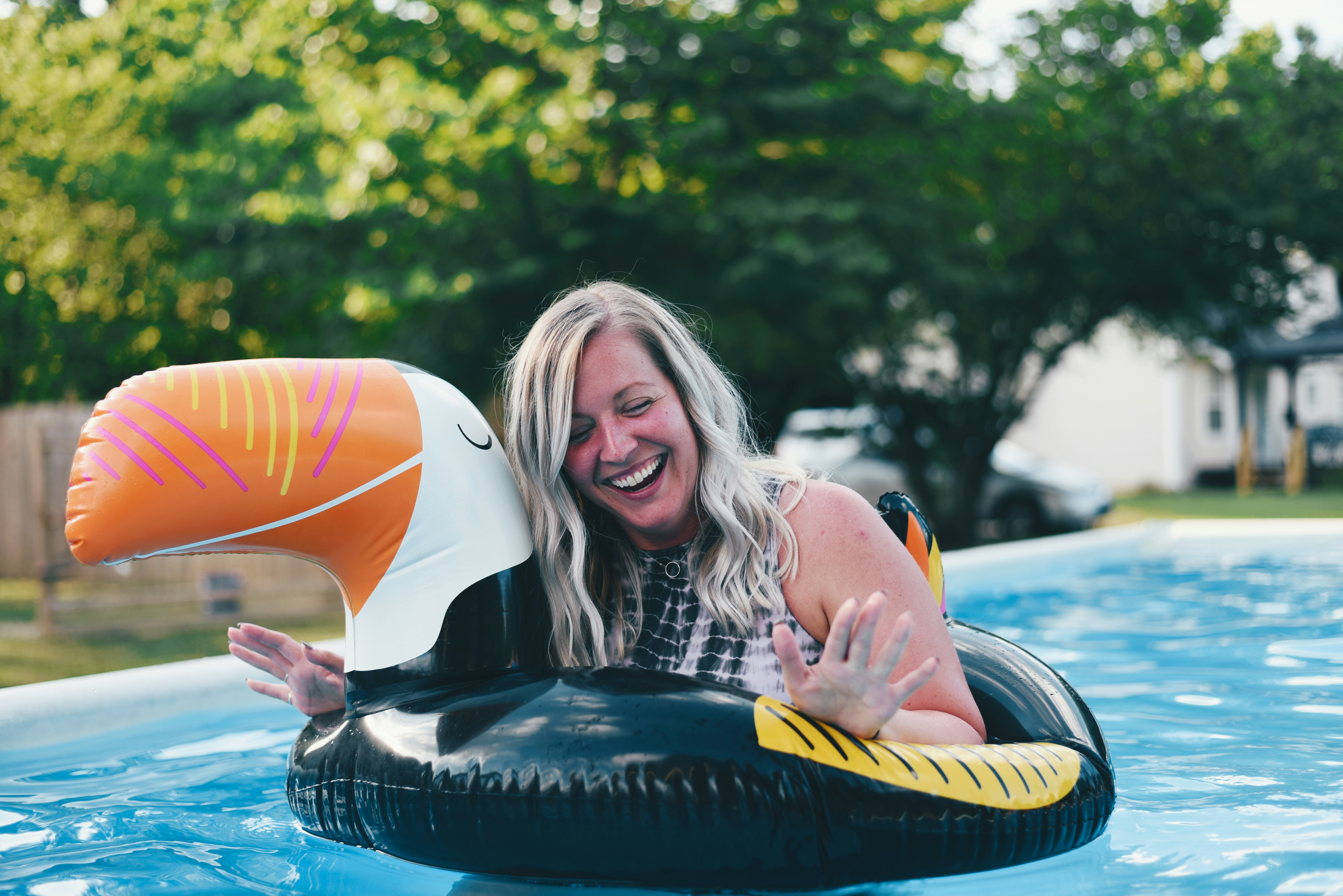 Woman laughing and enjoying herself while lounging on a toucan-shaped inflatable in a swimming pool.