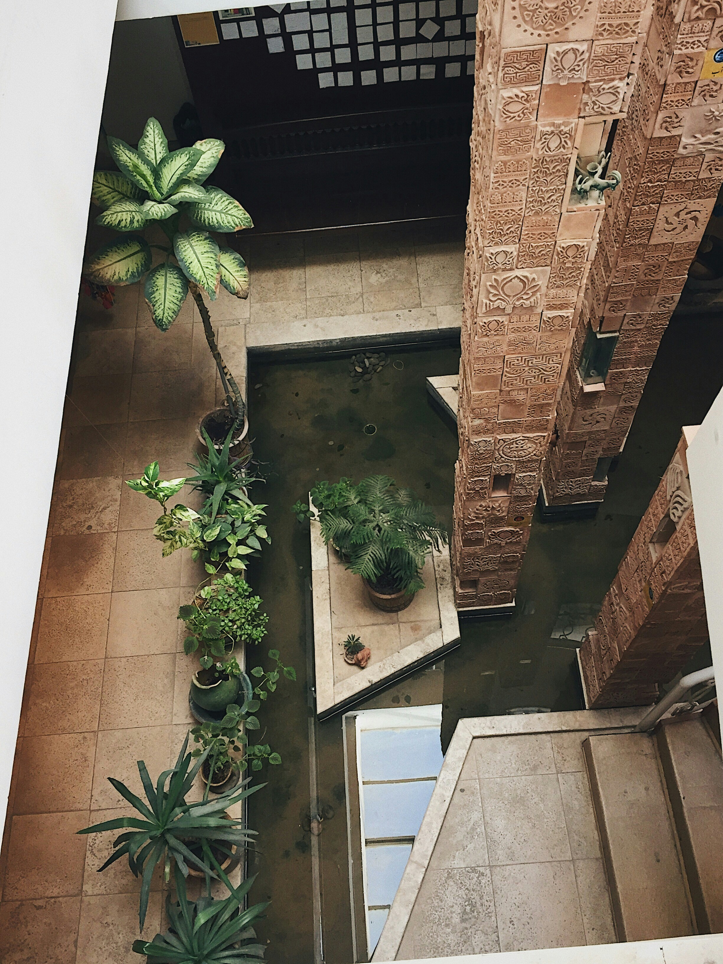 Indoor garden featuring lush greenery and a tranquil water feature surrounded by intricately designed stone pillars.