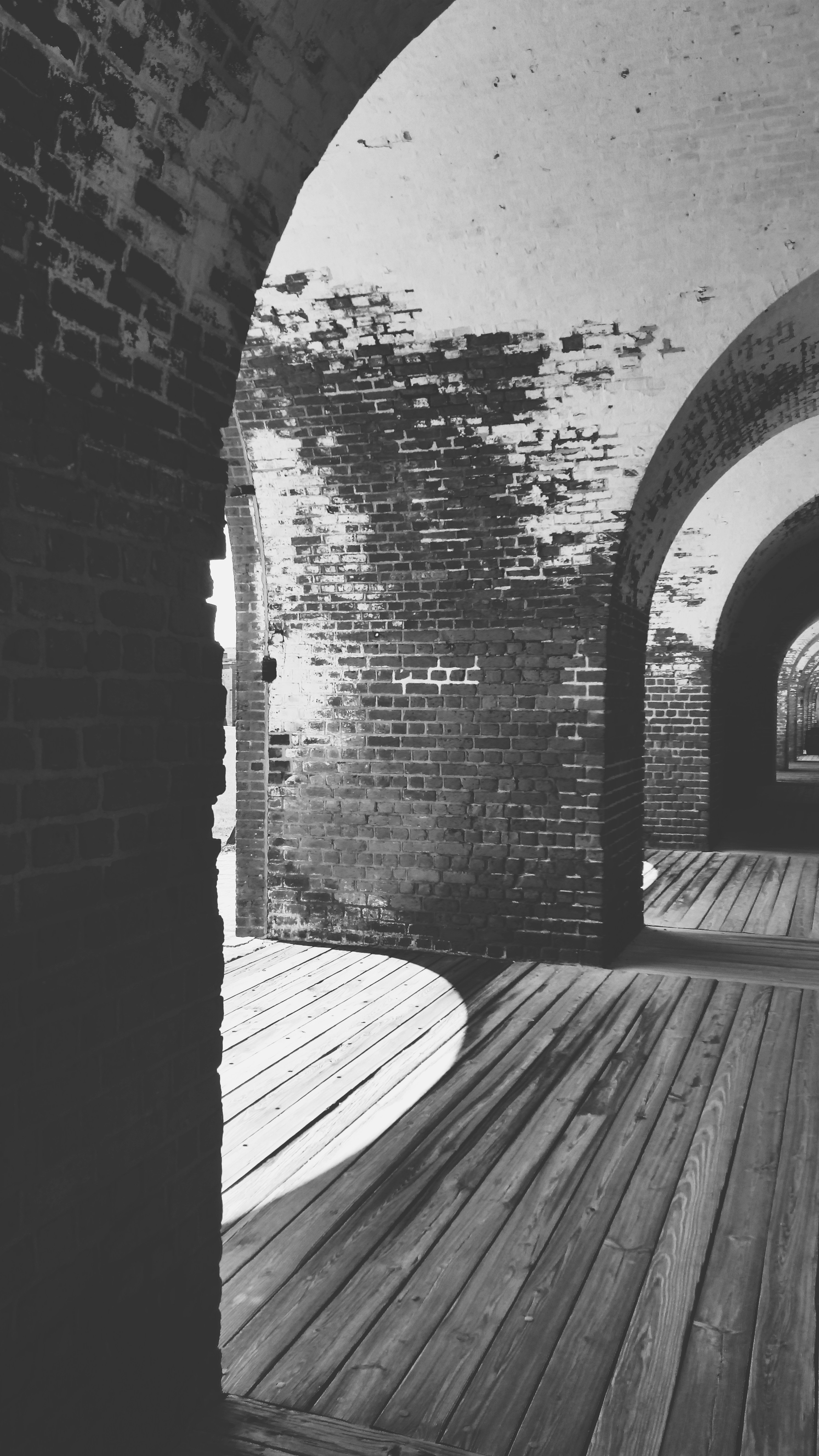 Monochrome view of a series of arched brick corridors with wooden flooring, creating a sense of depth and history.