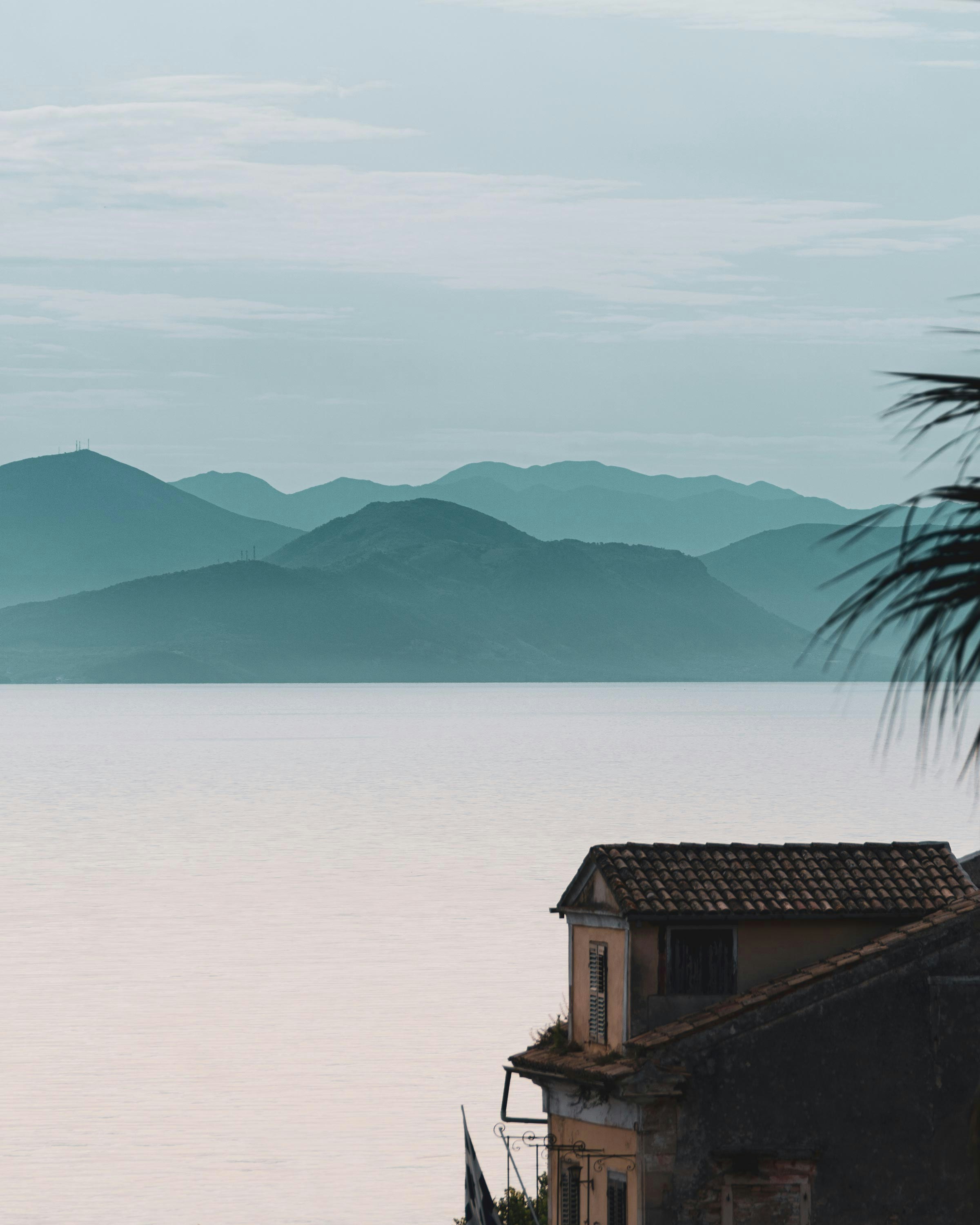 Serene coastal scene with distant mountains and a rustic building in the foreground at dawn.