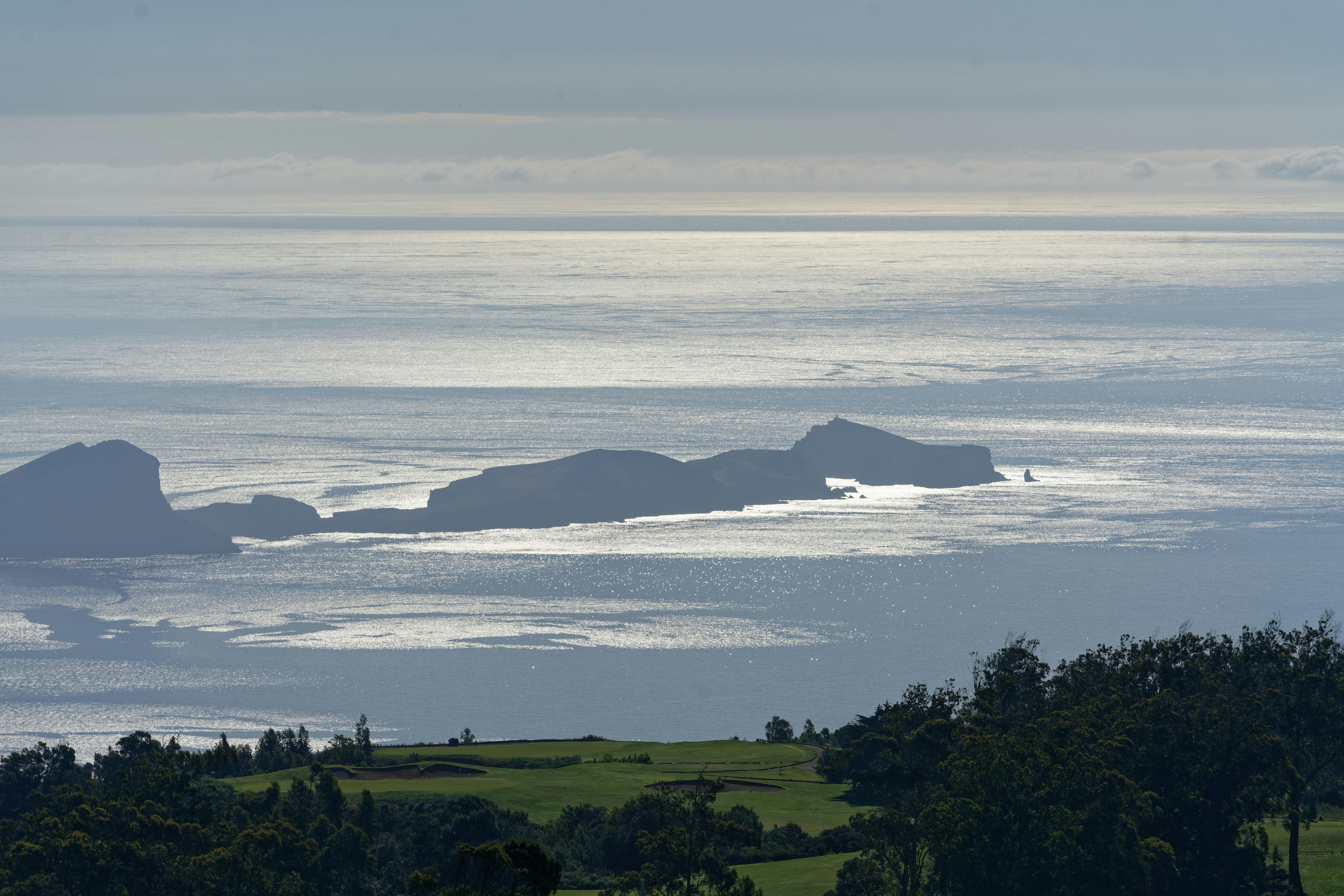Distant islands silhouetted against a shimmering sea under a hazy sky, capturing the tranquility of the coastline.