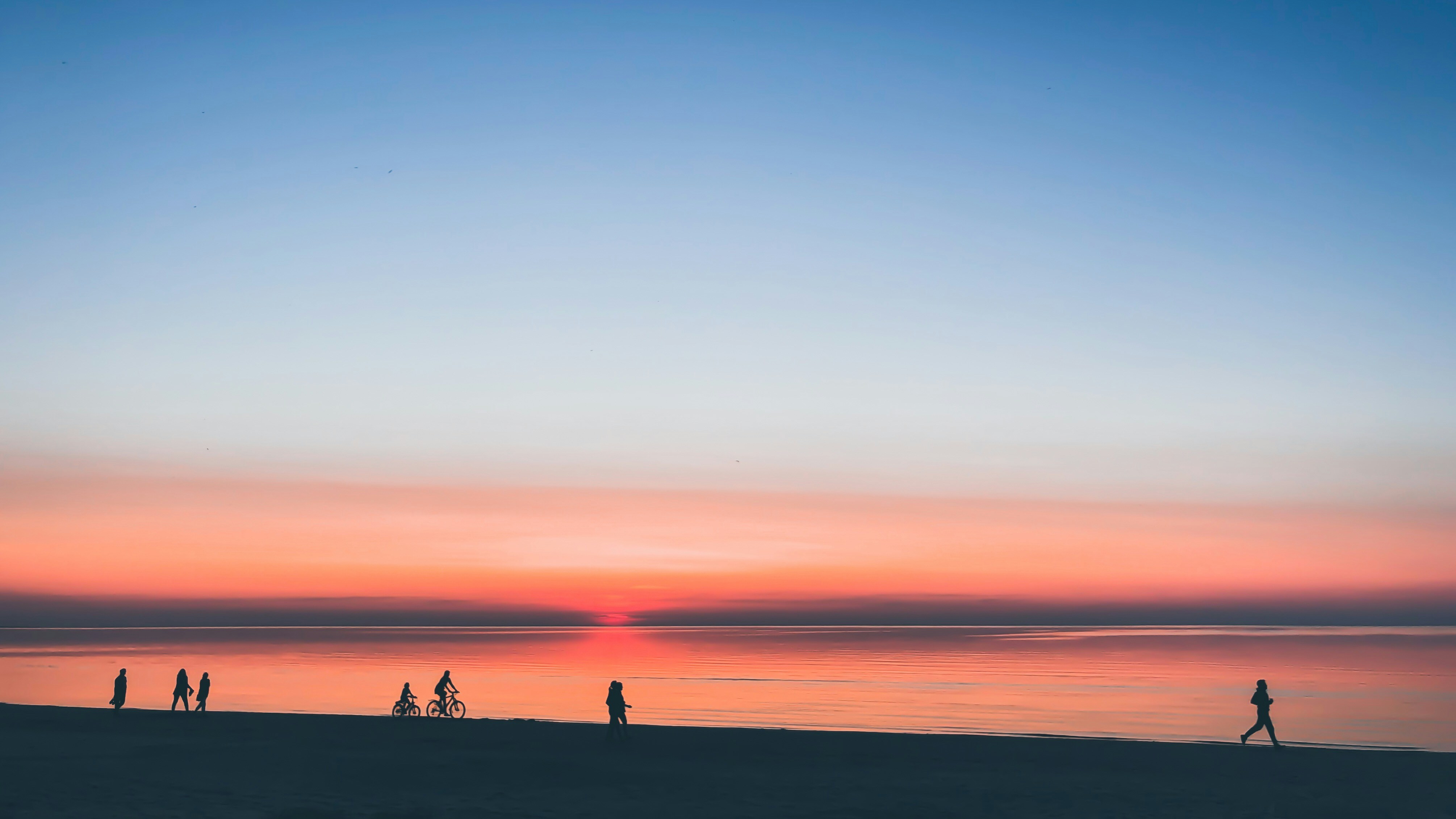 Silhouetted figures stroll along a tranquil beach at sunset with a gradient sky transitioning from orange to blue.