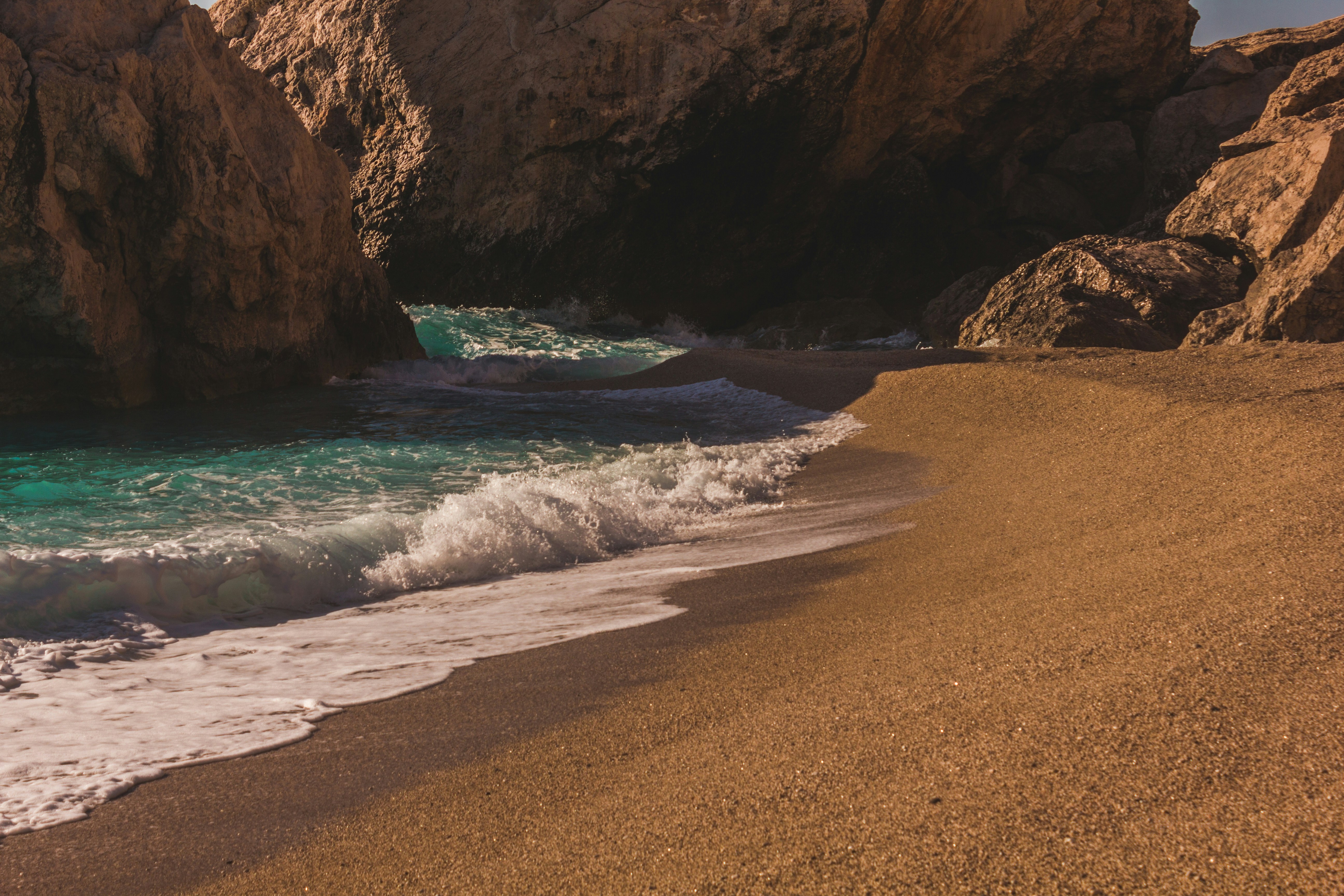 Gentle waves caress a sandy beach framed by rugged cliffs under the golden light of late afternoon.