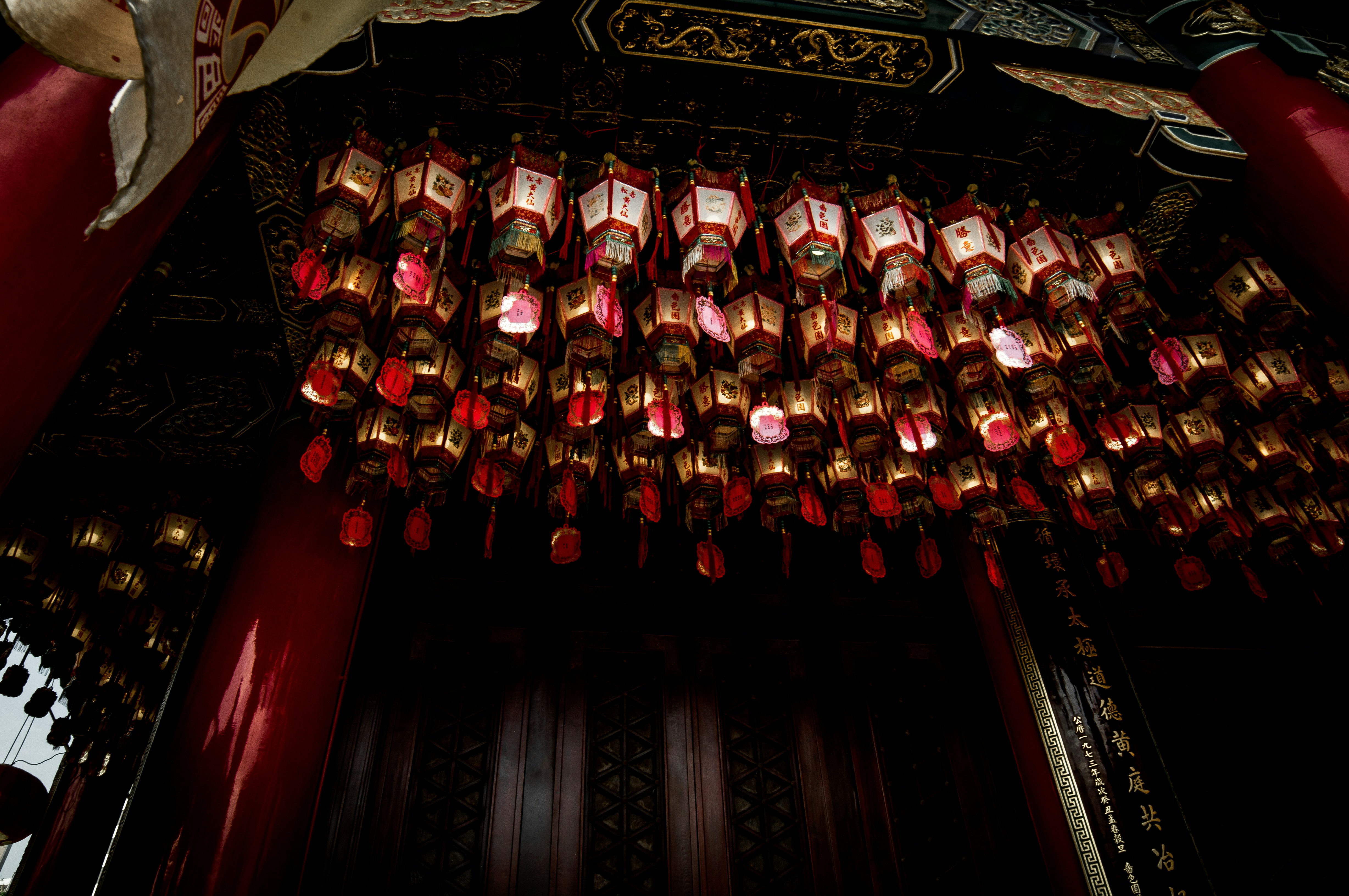 Photograph of numerous red lanterns suspended from an elaborately decorated ceiling inside a traditional Chinese temple.