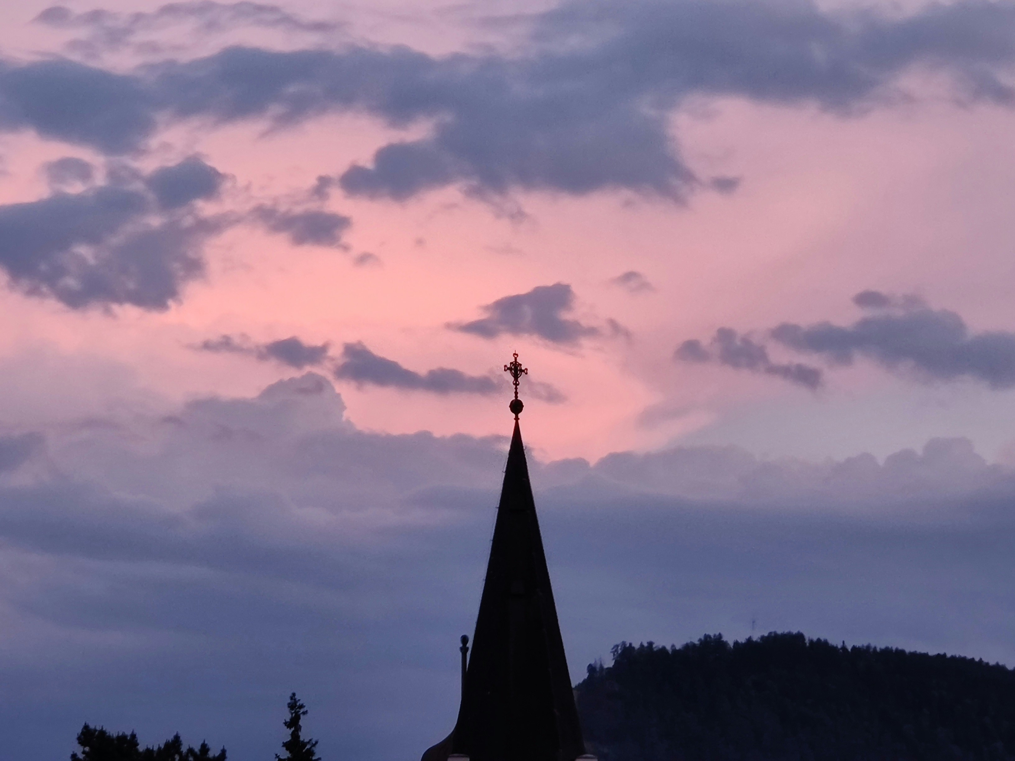 Church spire silhouetted against a pink and purple sunset sky with scattered clouds.